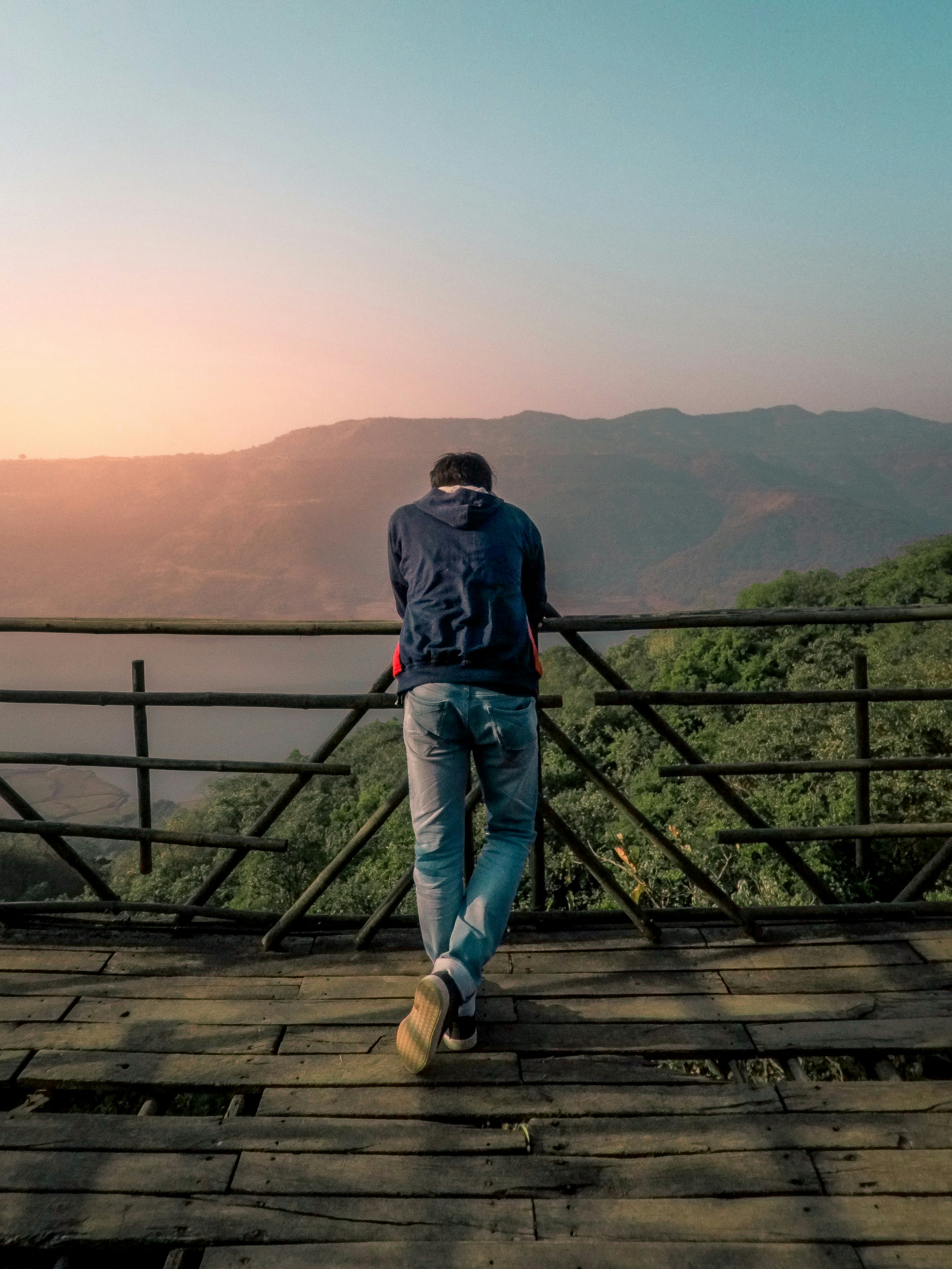Horizon Gate: A lone figure leans on a wooden railing at dusk, overlooking rolling valleys