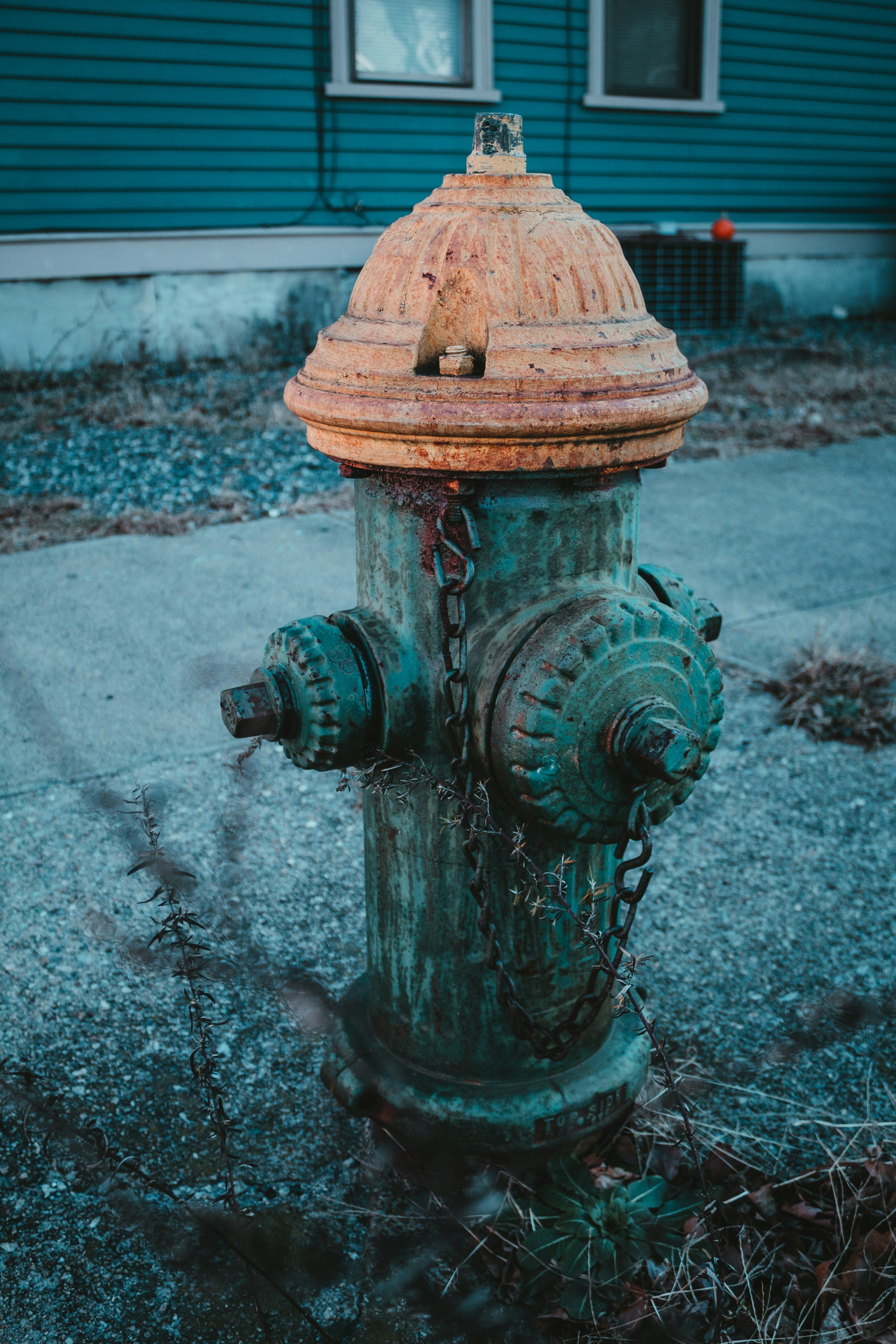 Weathered fire hydrant adorned with chains, standing guard on a quiet street. Its vibrant patina tells stories of time and use.