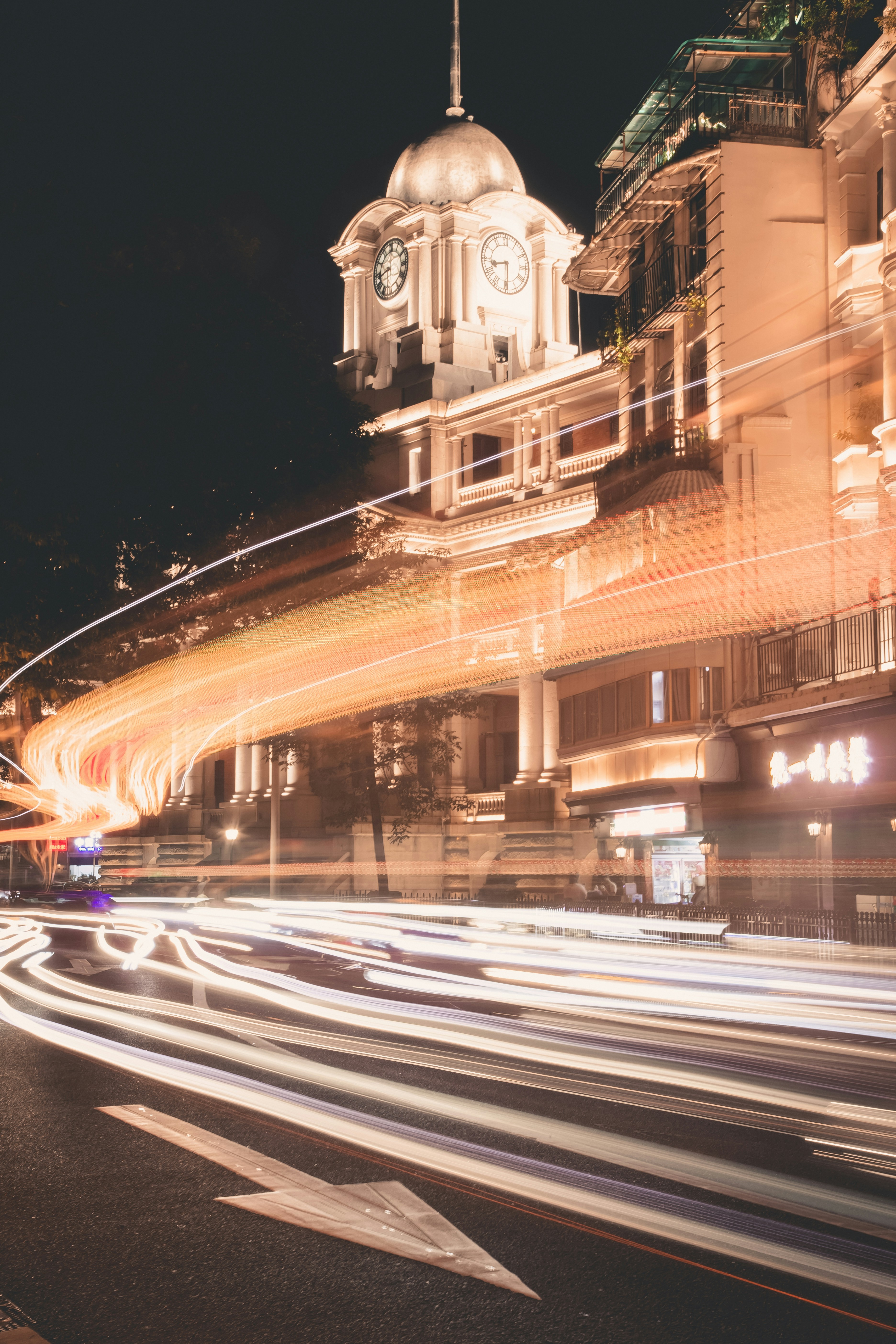 Historic clock tower illuminated against a backdrop of dynamic light trails from passing vehicles at night.