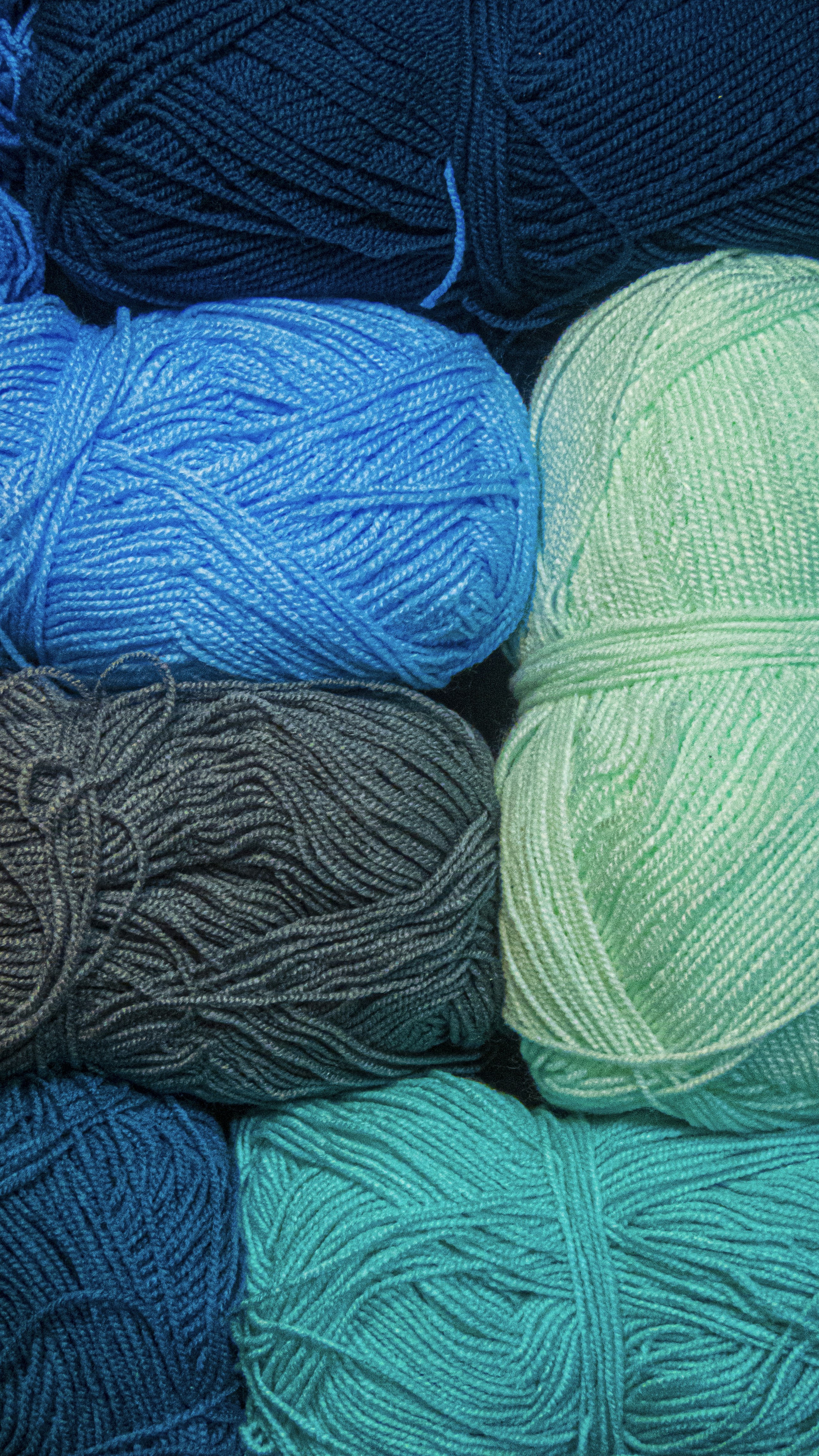 A vibrant arrangement of yarn skeins in various shades of blue and green, showcasing their textures and colors against a dark background.