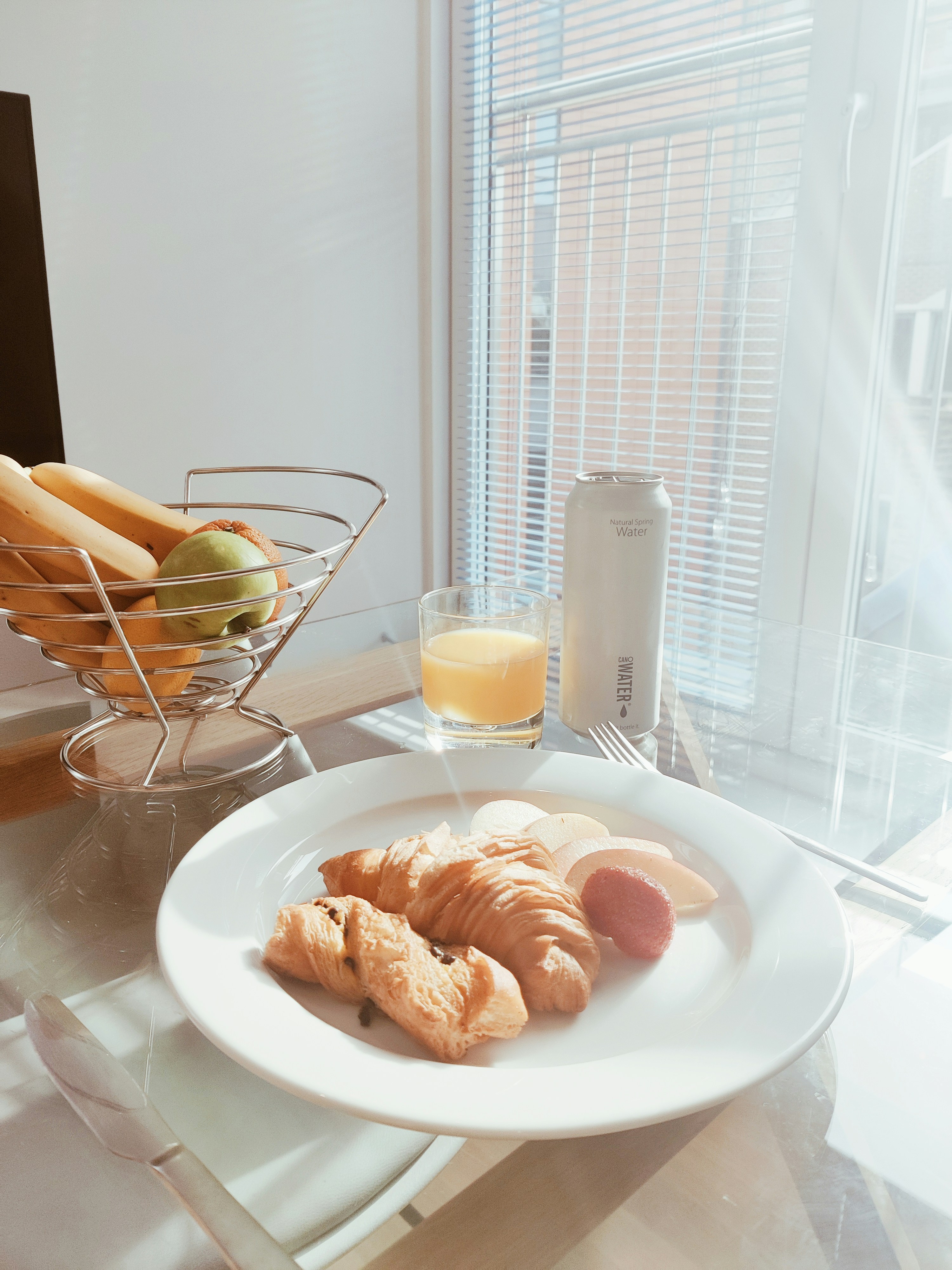Sunlit Breakfast Plate: Croissants, Fruit, and Orange Juice by the Window