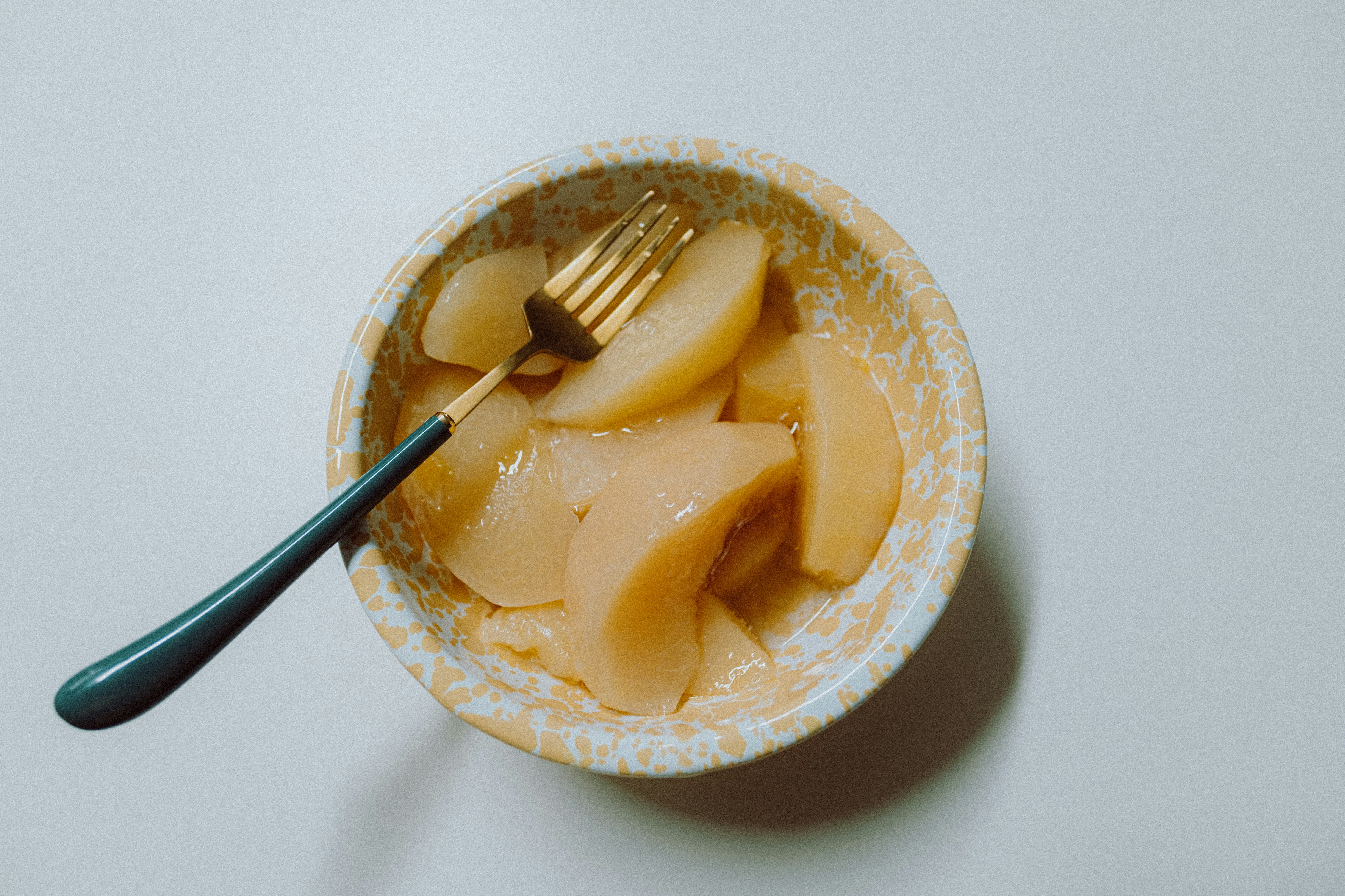 Overhead Peach Halves in a Speckled Ceramic Bowl, a Teal Fork Resting Across the Fruit