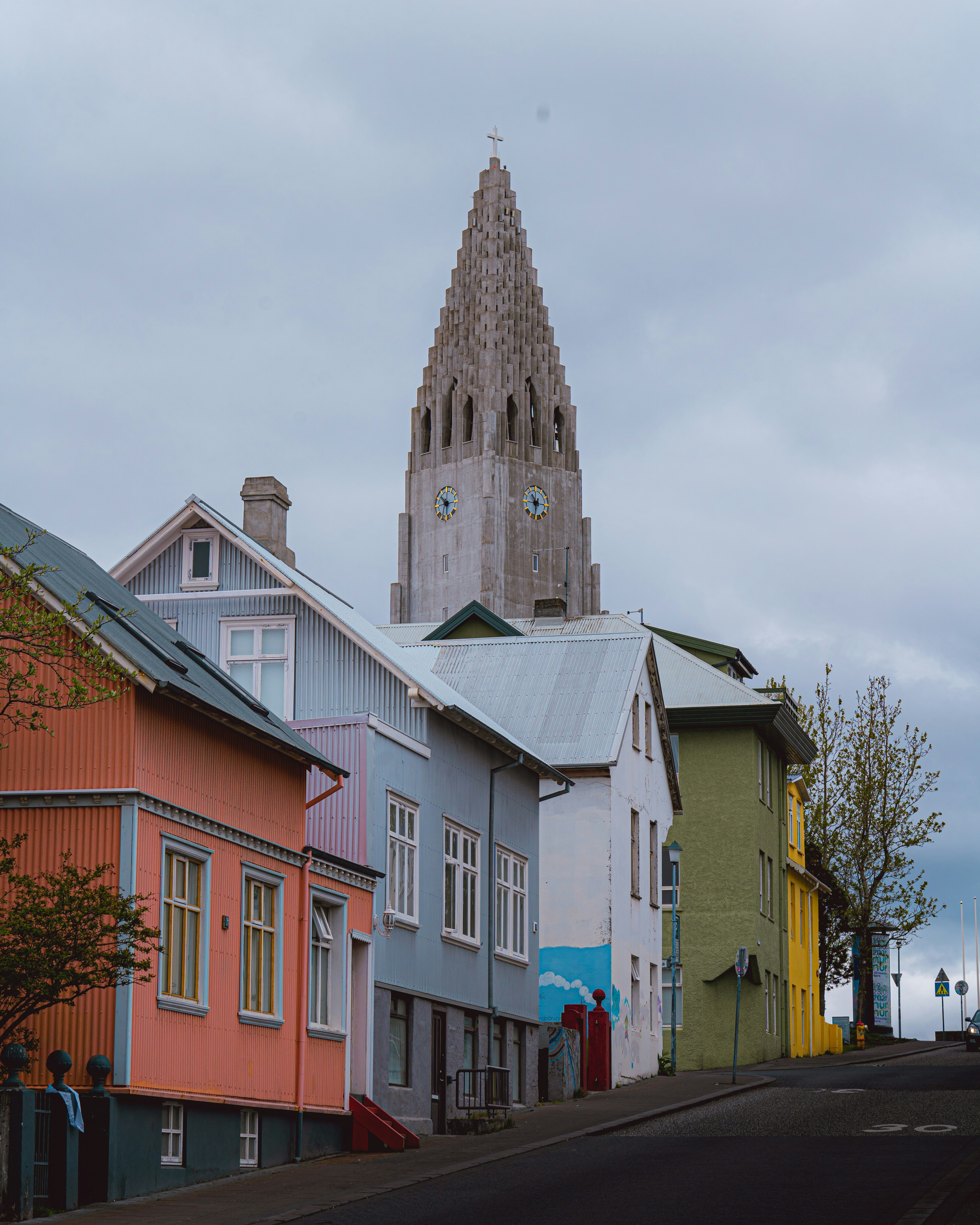 Vibrant houses line a sloping street, with a prominent church tower rising in the background against a moody sky.