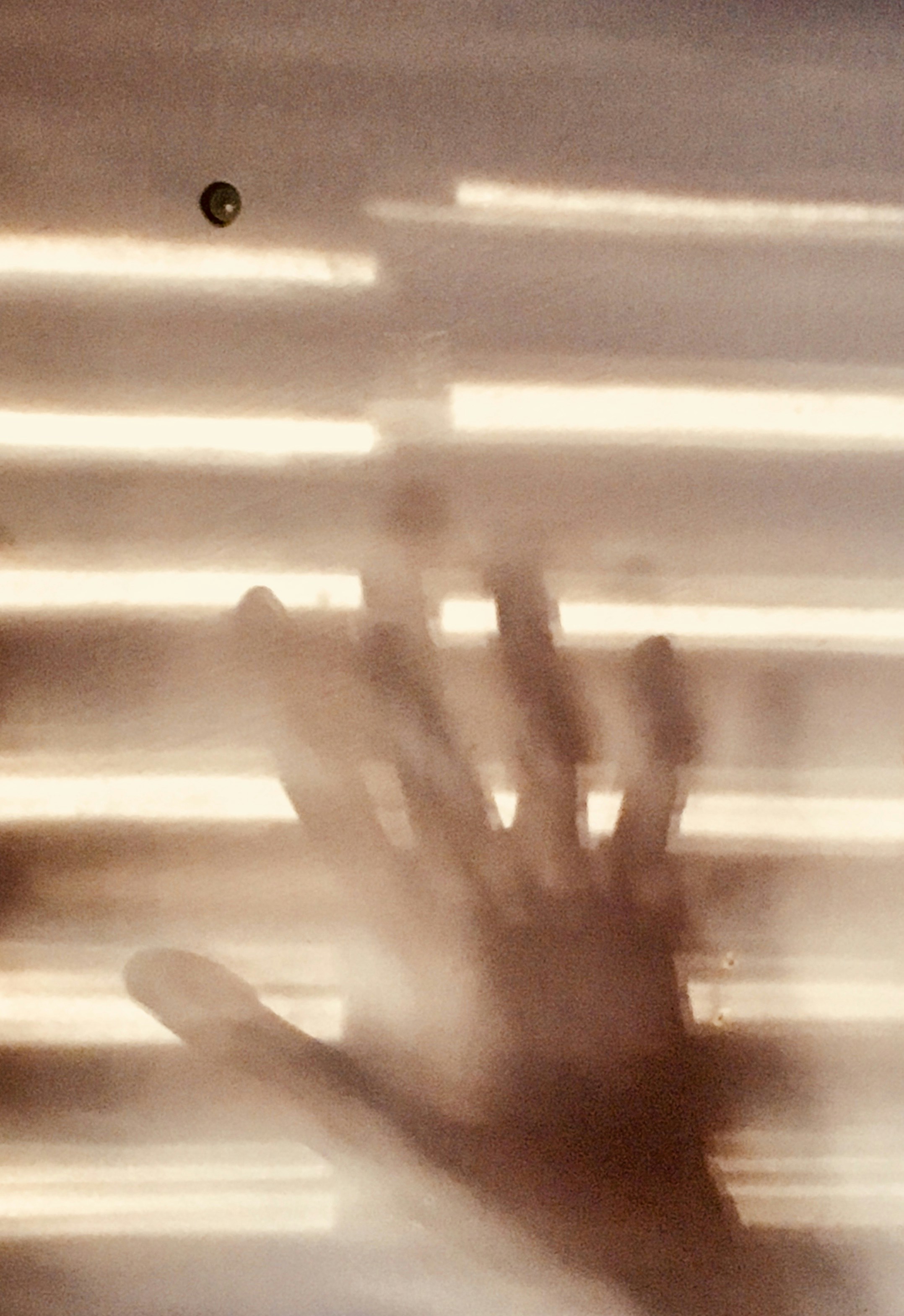 A hand pressed against a translucent surface, casting a soft shadow amidst horizontal light streaks. The interplay of light and form creates a sense of depth.