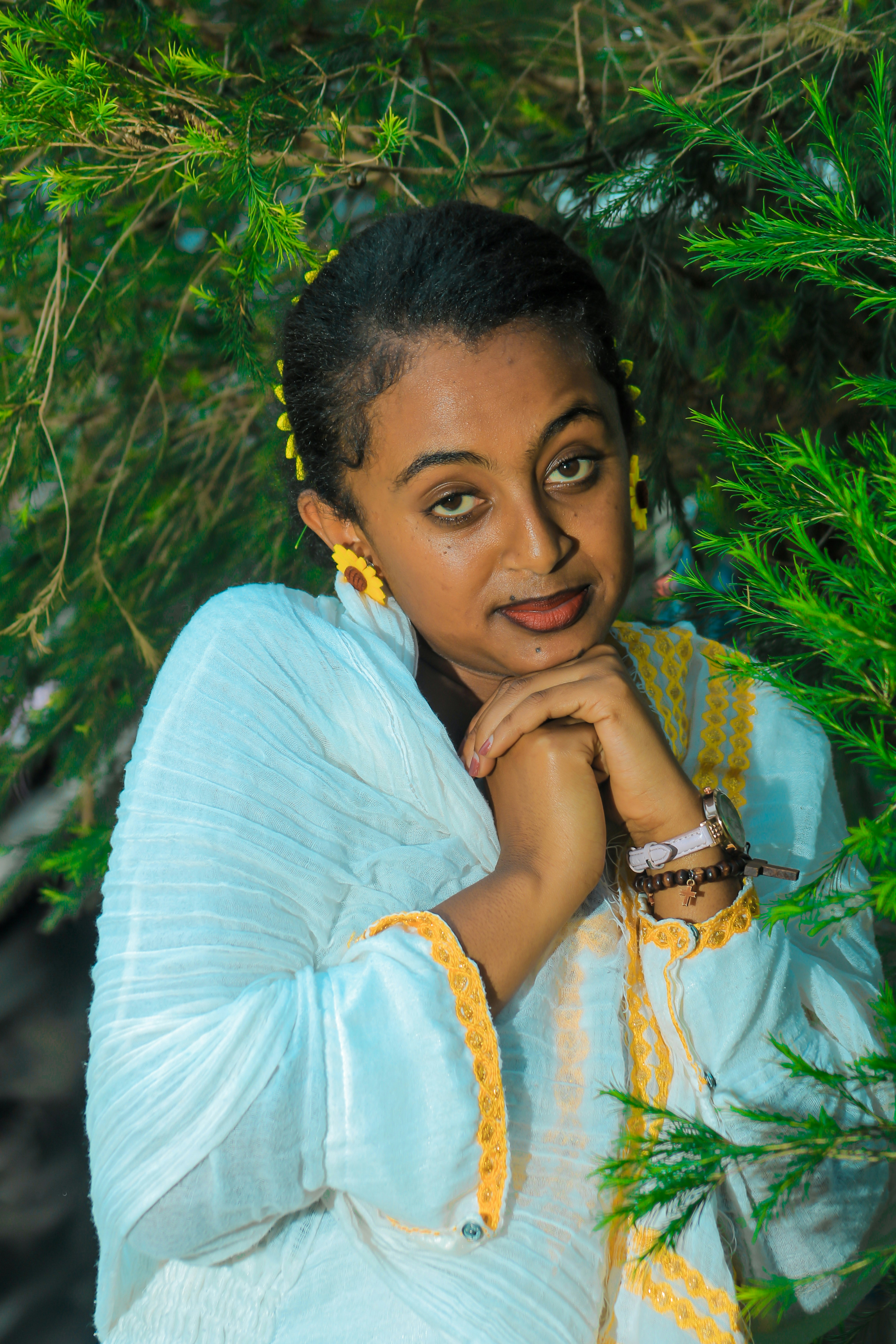 A young woman in a light blue garment poses thoughtfully among lush greenery, exuding a sense of calm and connection with nature.