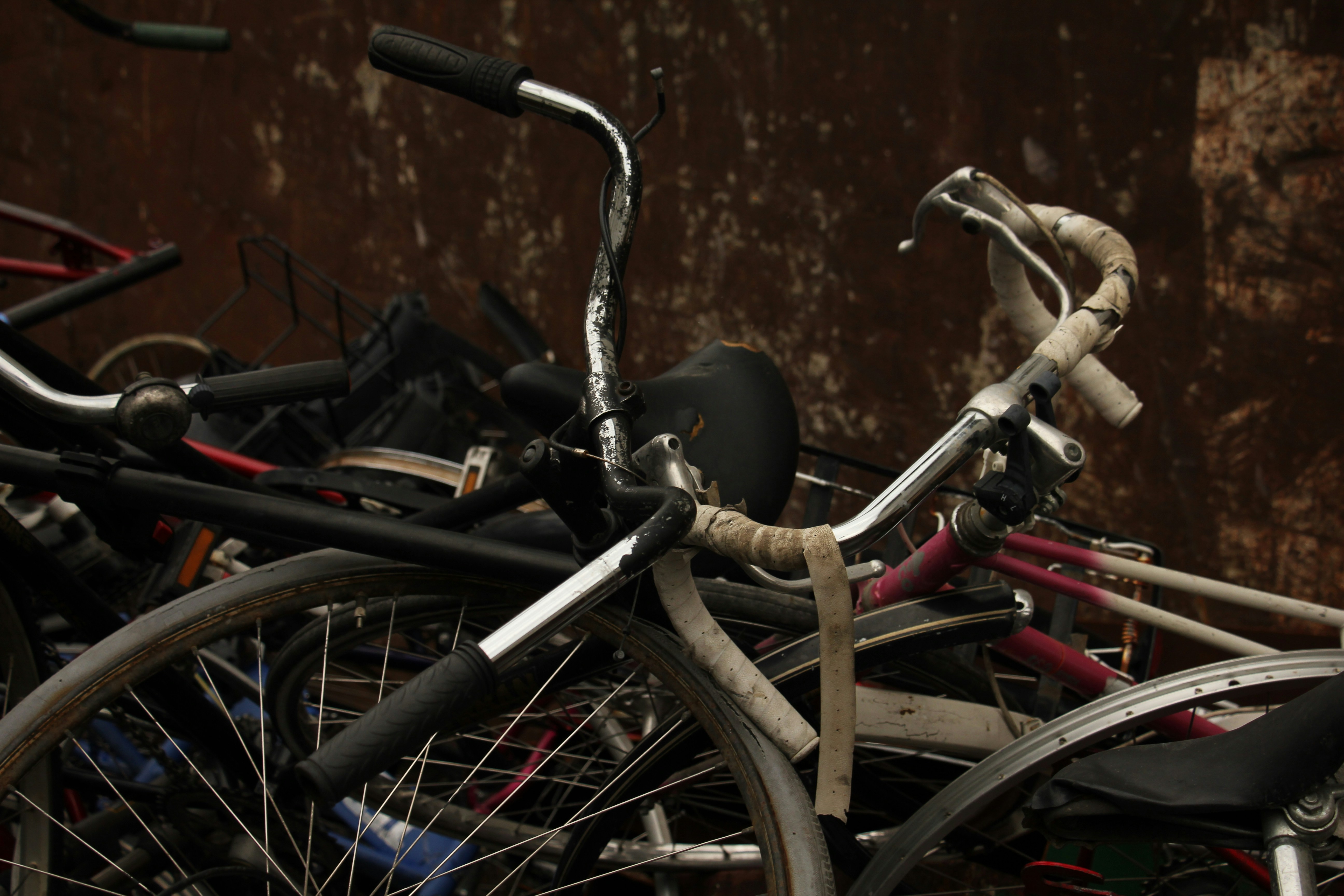 A collection of neglected bicycles stacked together, showcasing their worn handles and rusted frames against a weathered backdrop.