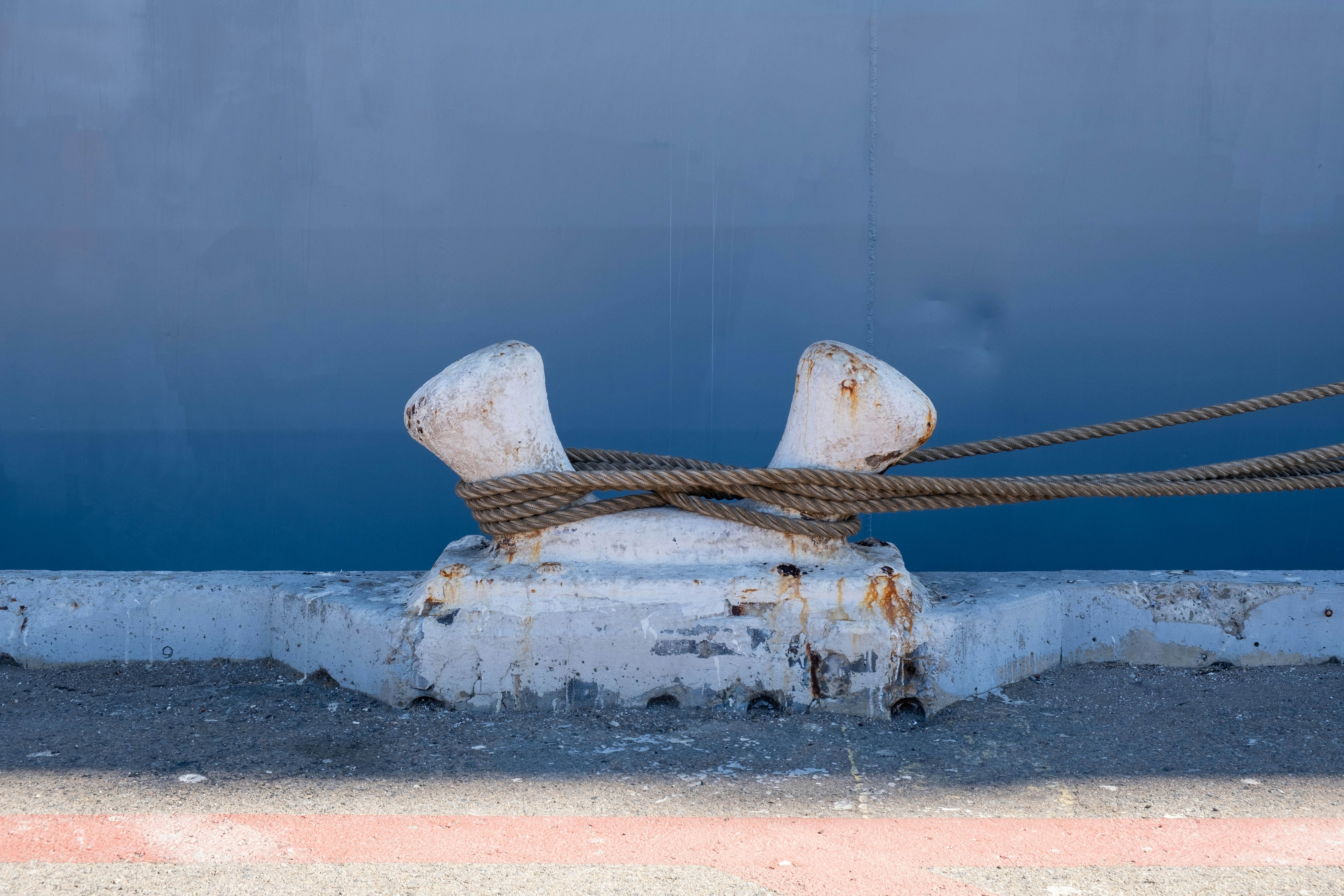 Weathered bollard secured with thick rope against a textured blue background, highlighting maritime elements. 