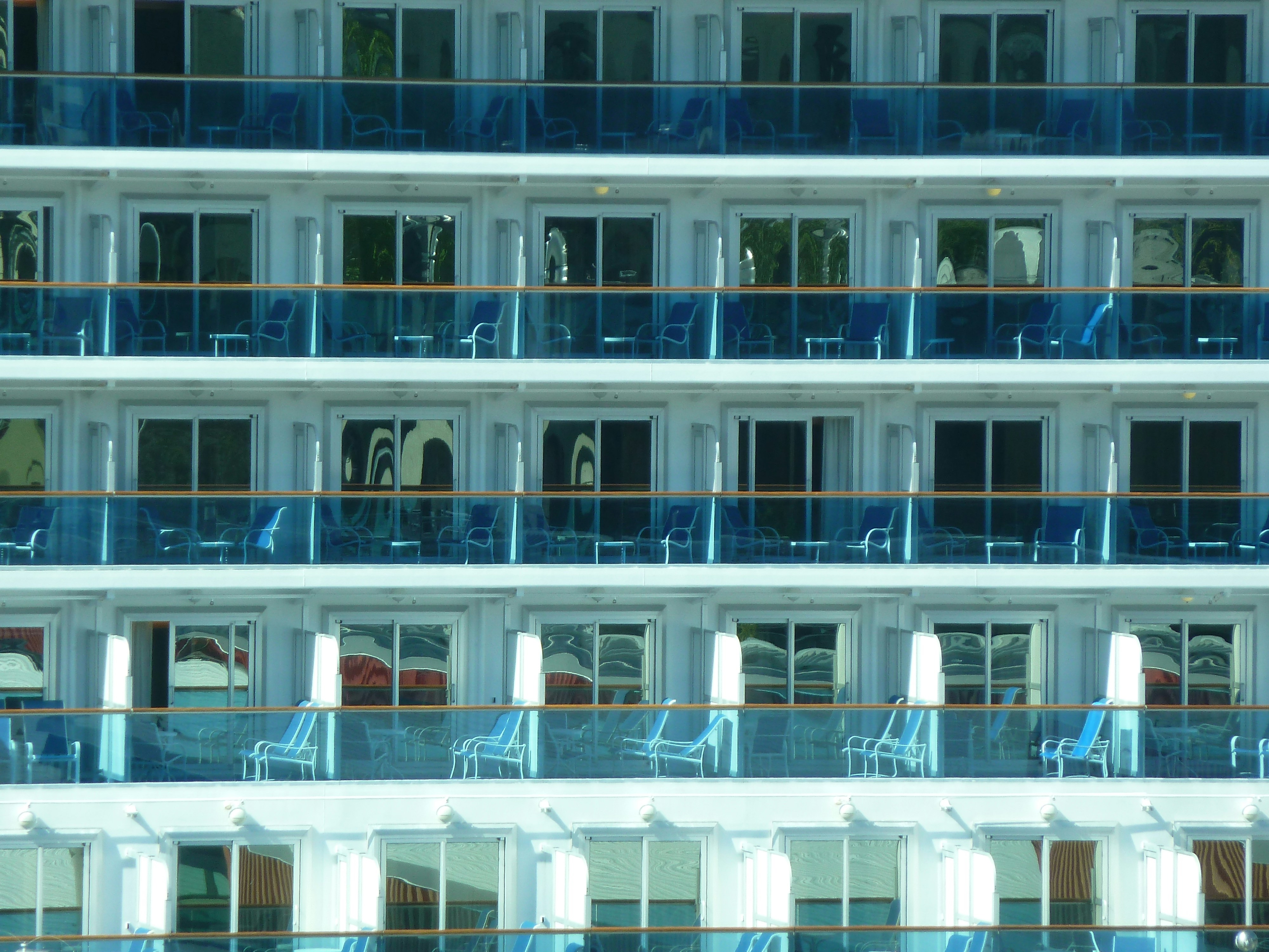 Balconies of a cruise ship reflecting sunlight, showcasing a pattern of blue and white elements. The scene highlights the interplay of light and architecture.