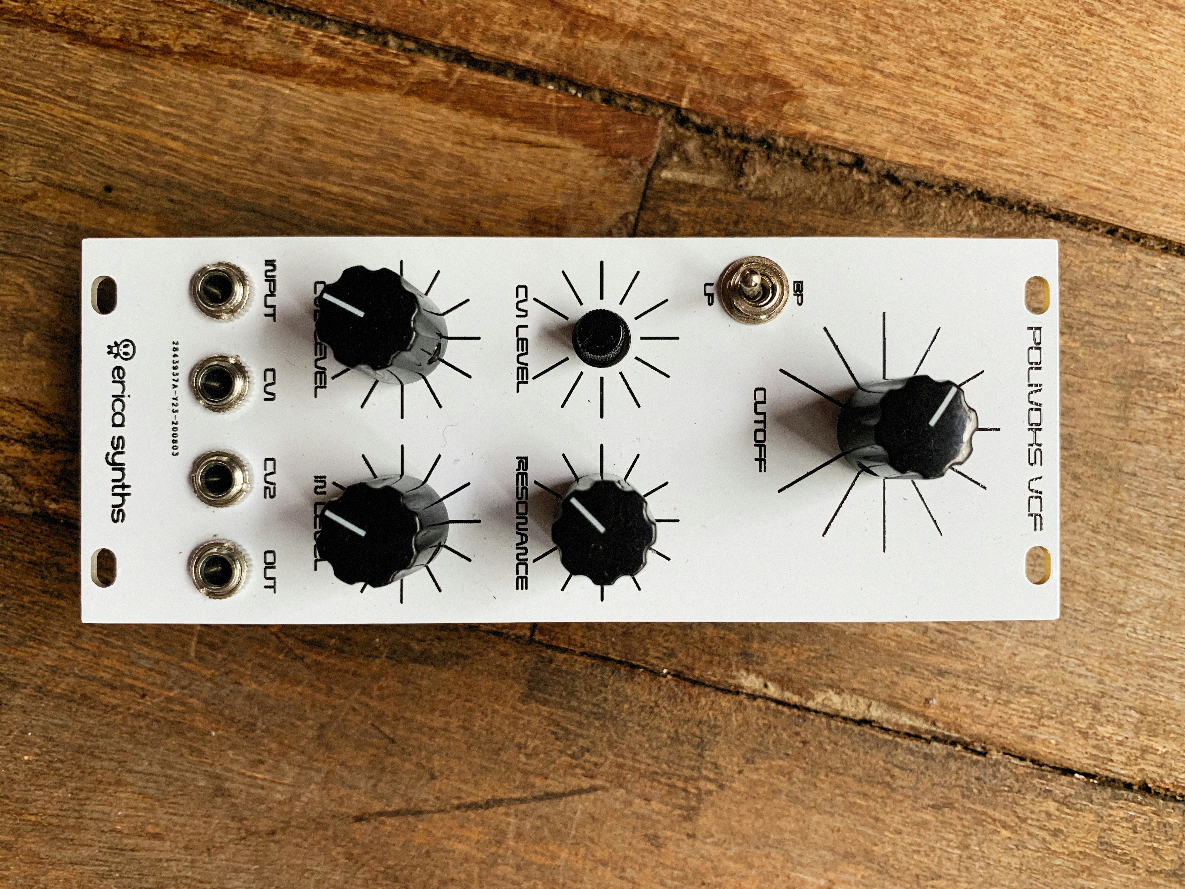 Compact white guitar pedal with black knobs and radial dial markings rests on a weathered wooden surface.