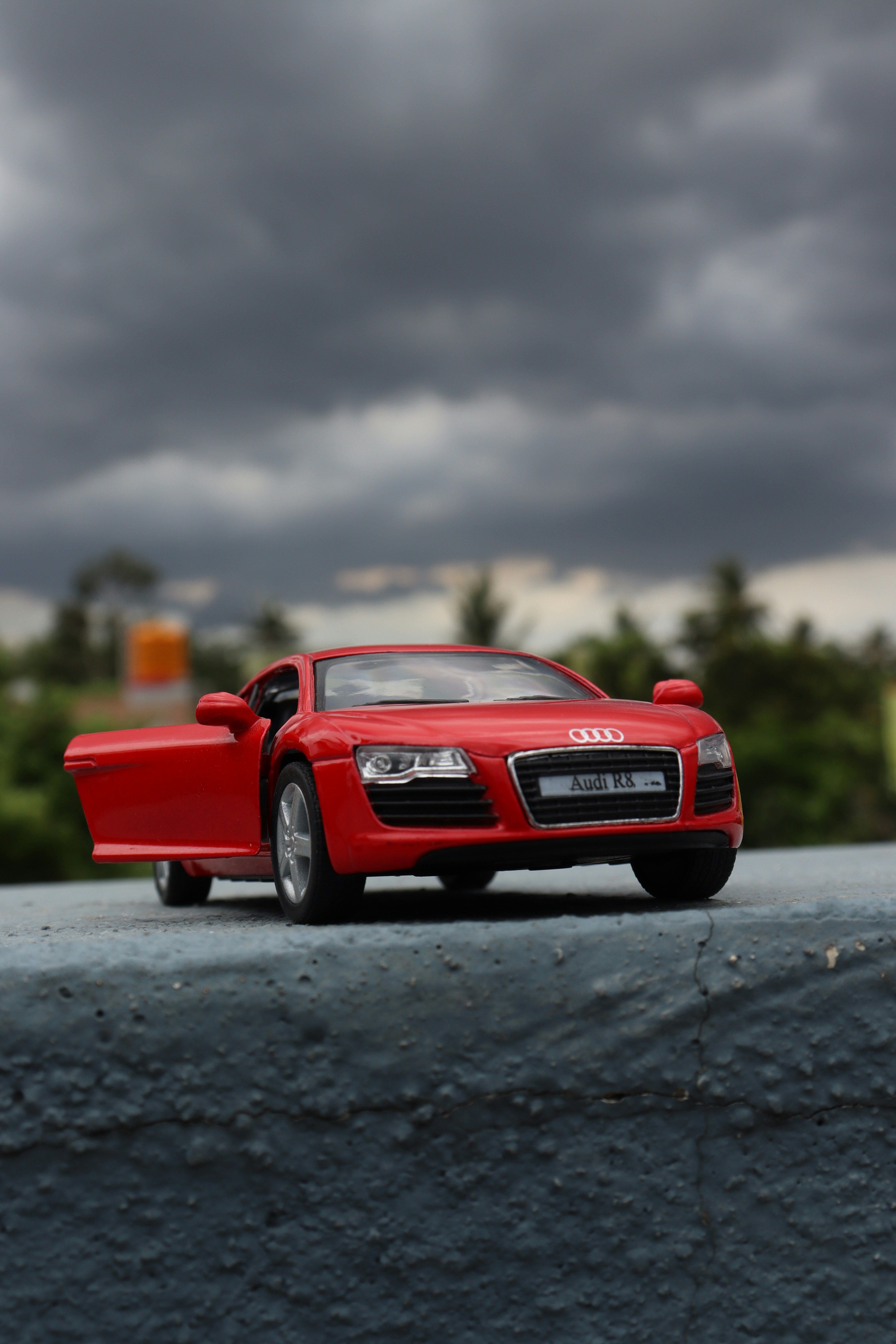 Miniature Red Audi R8 on a Weathered Blue Barrier Beneath Stormy Skies