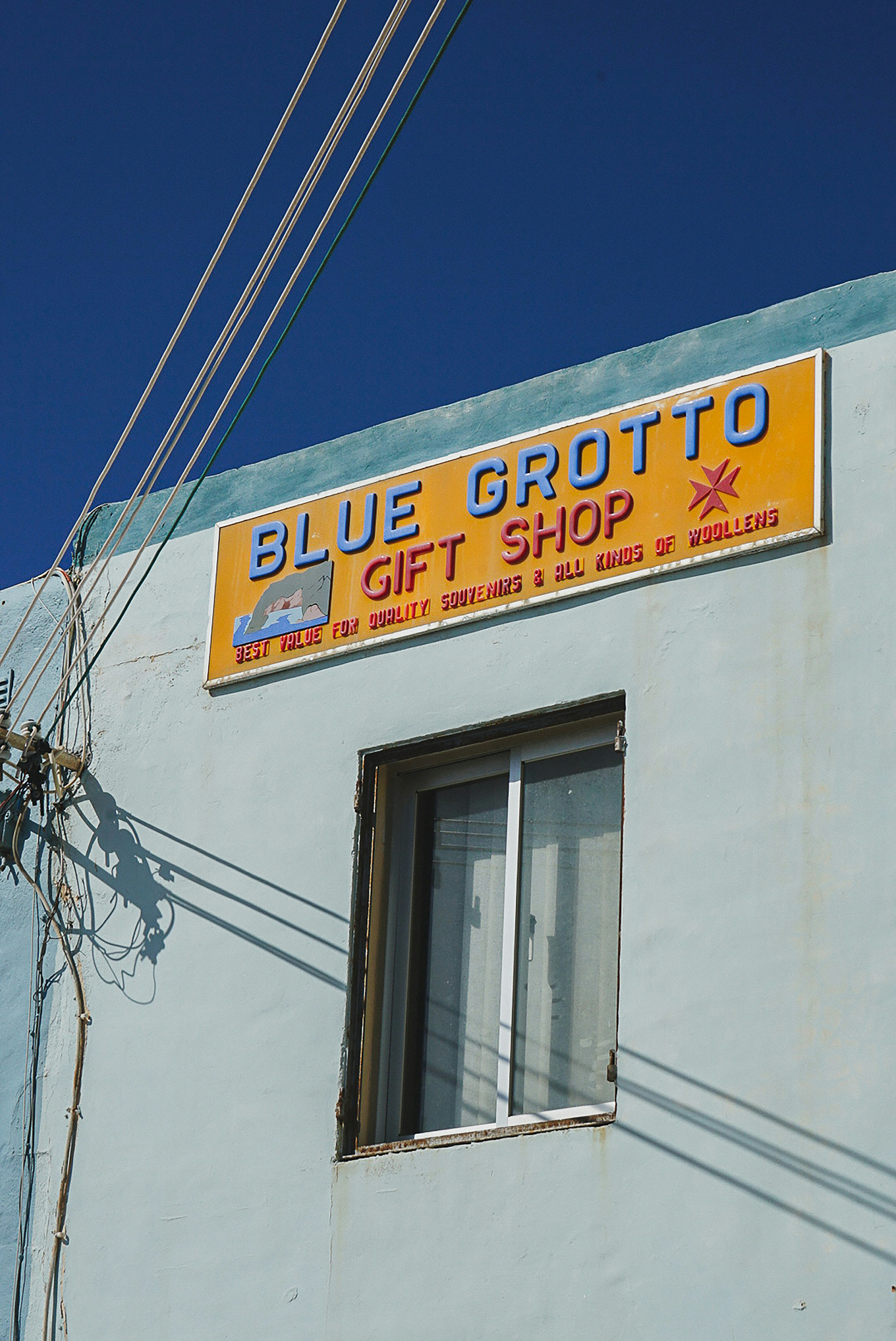 Blue Grotto Gift Shop: Bright Orange Sign on a Sun-Washed Blue Wall