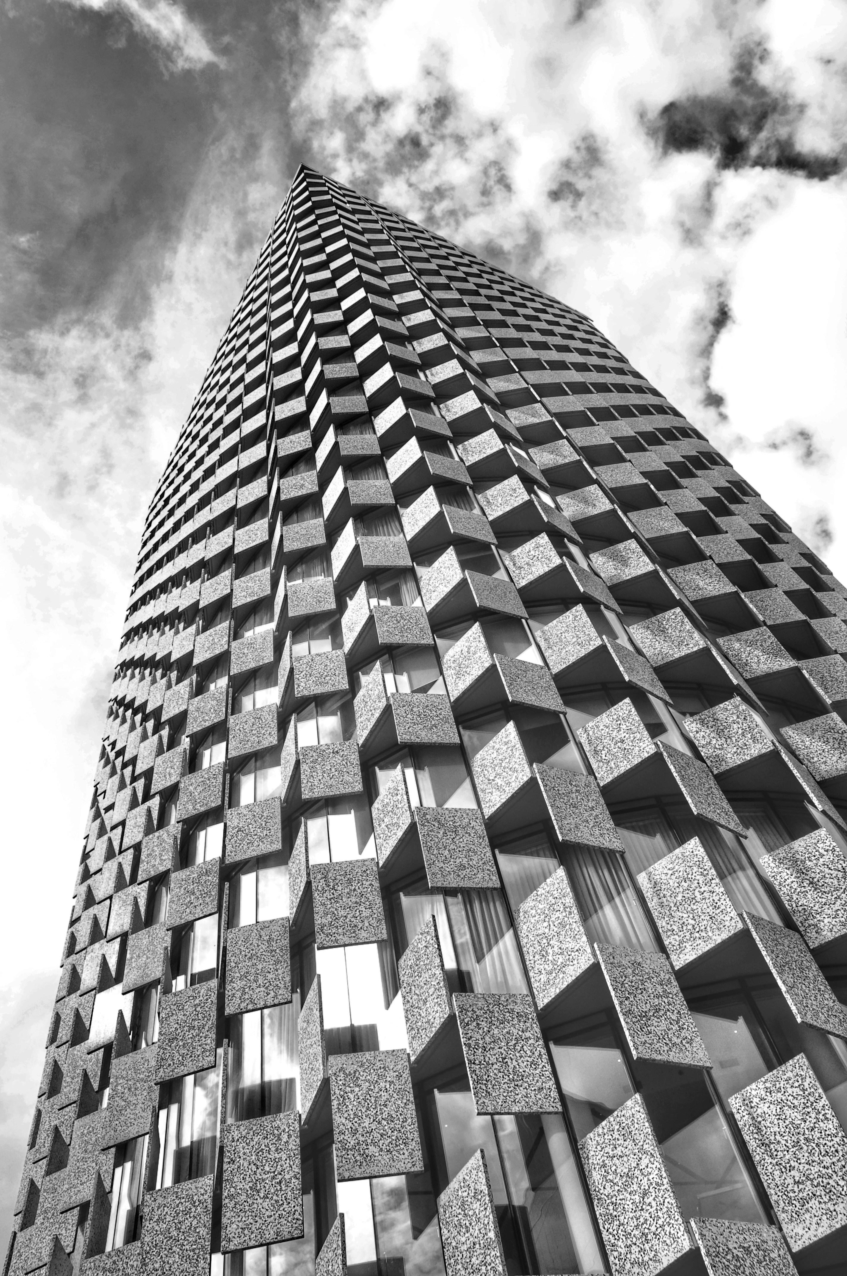 A modern architectural marvel with a textured facade, reaching towards the sky under a dramatic cloudscape.