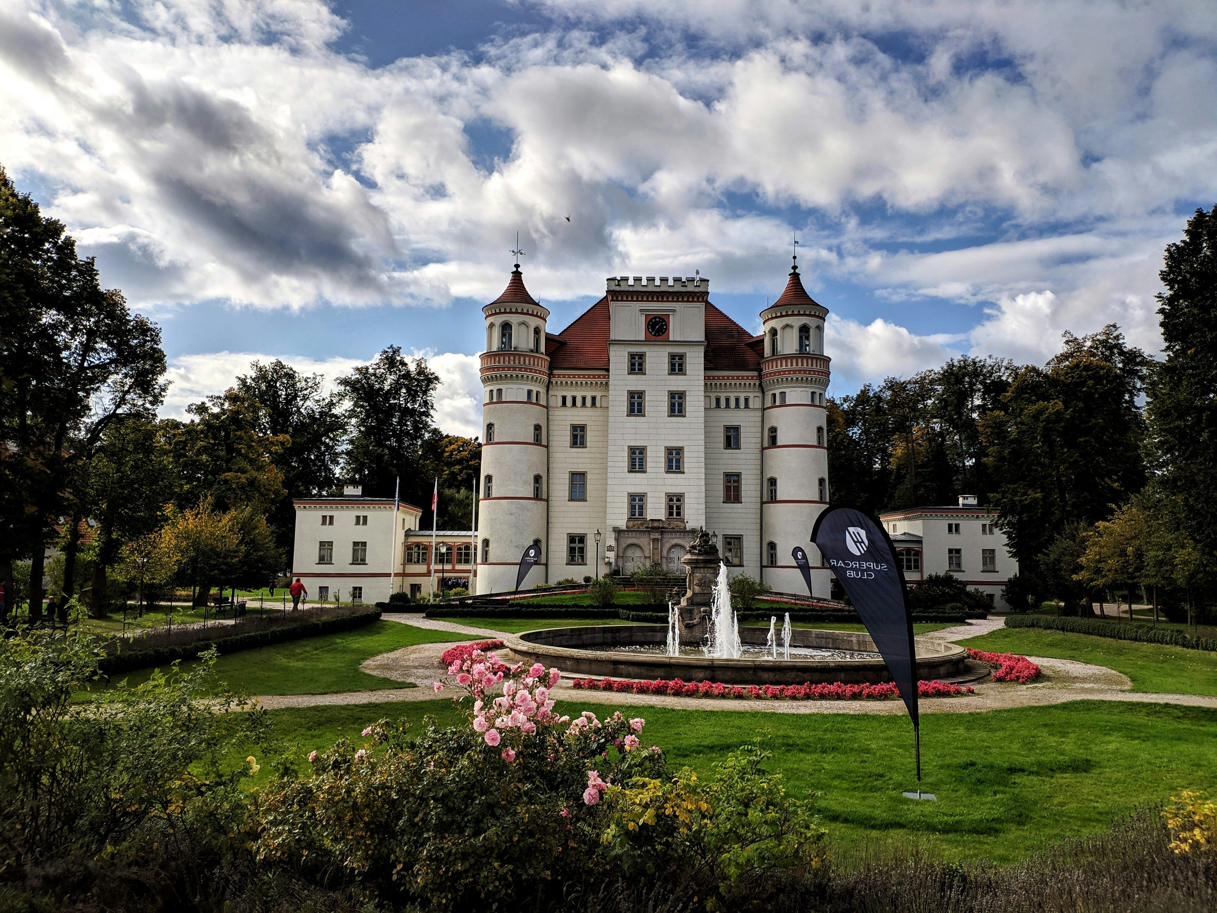 Historic castle surrounded by lush gardens and vibrant flowers, with a fountain at the center. Banners fluttering in the gentle breeze add a touch of elegance.