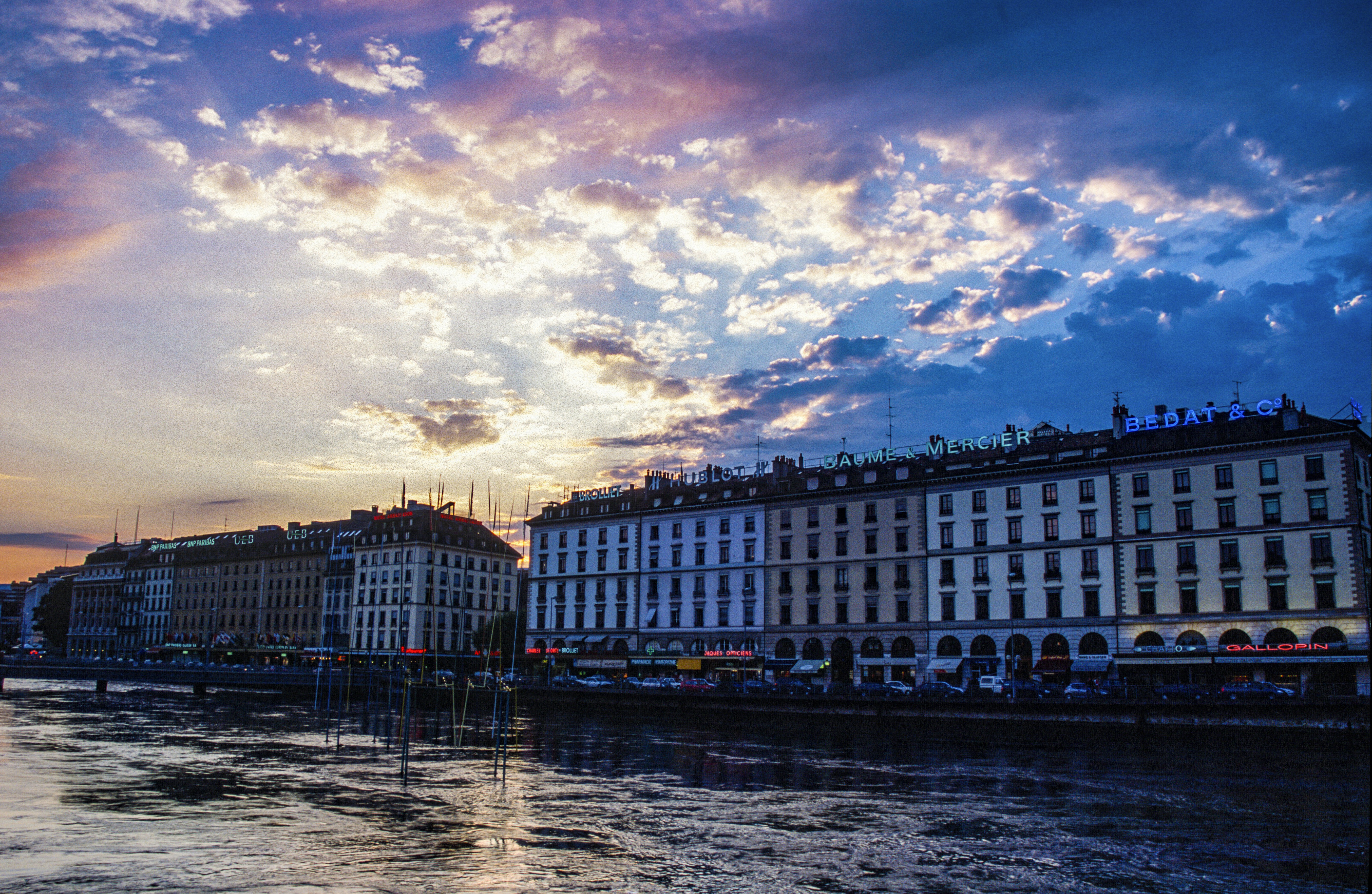 The sun is setting over the buildings along the water photo – Free ...
