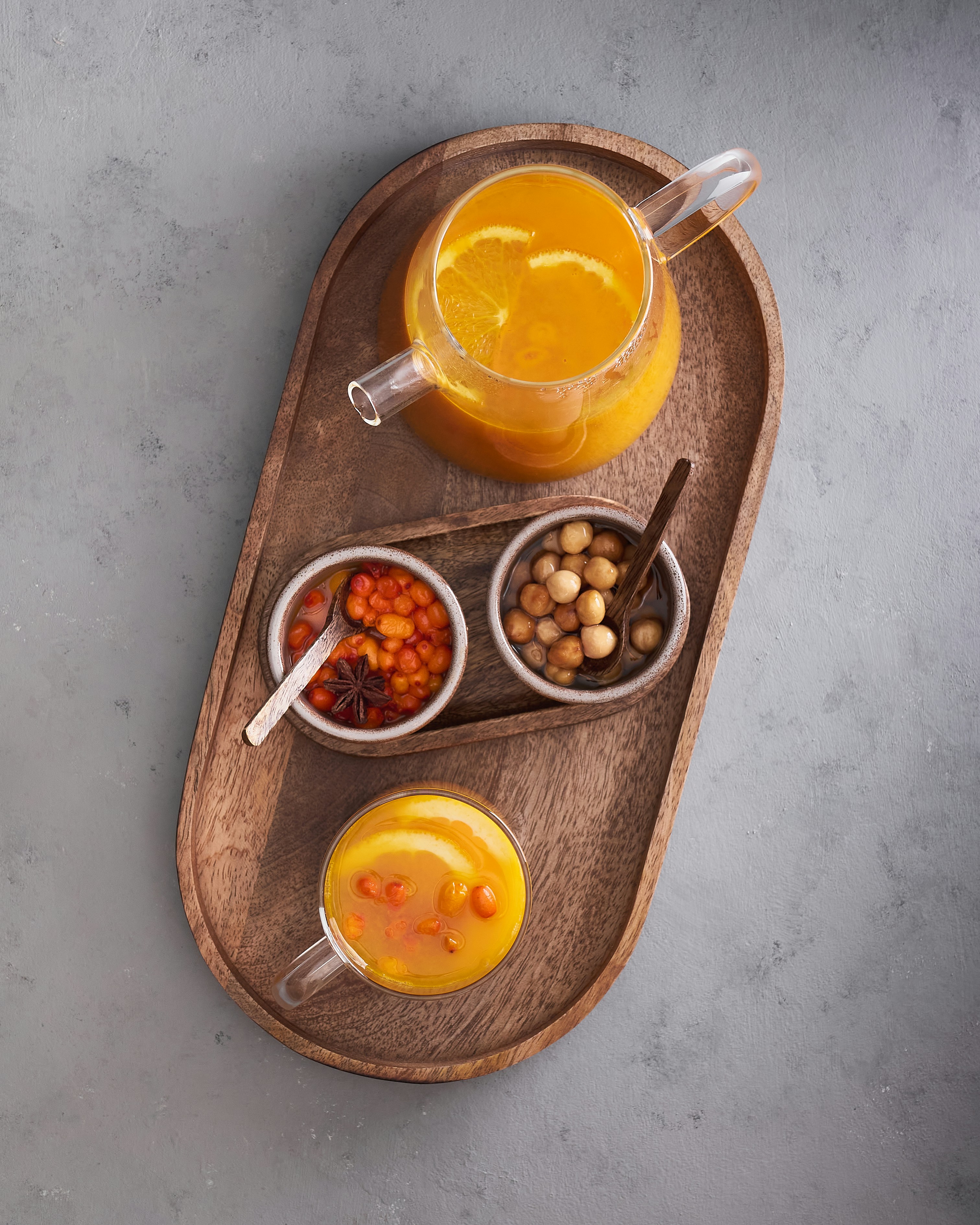 A wooden tray showcases a glass pitcher of orange beverage alongside bowls of vibrant berries and spices. The arrangement emphasizes a delightful fusion of colors and textures.