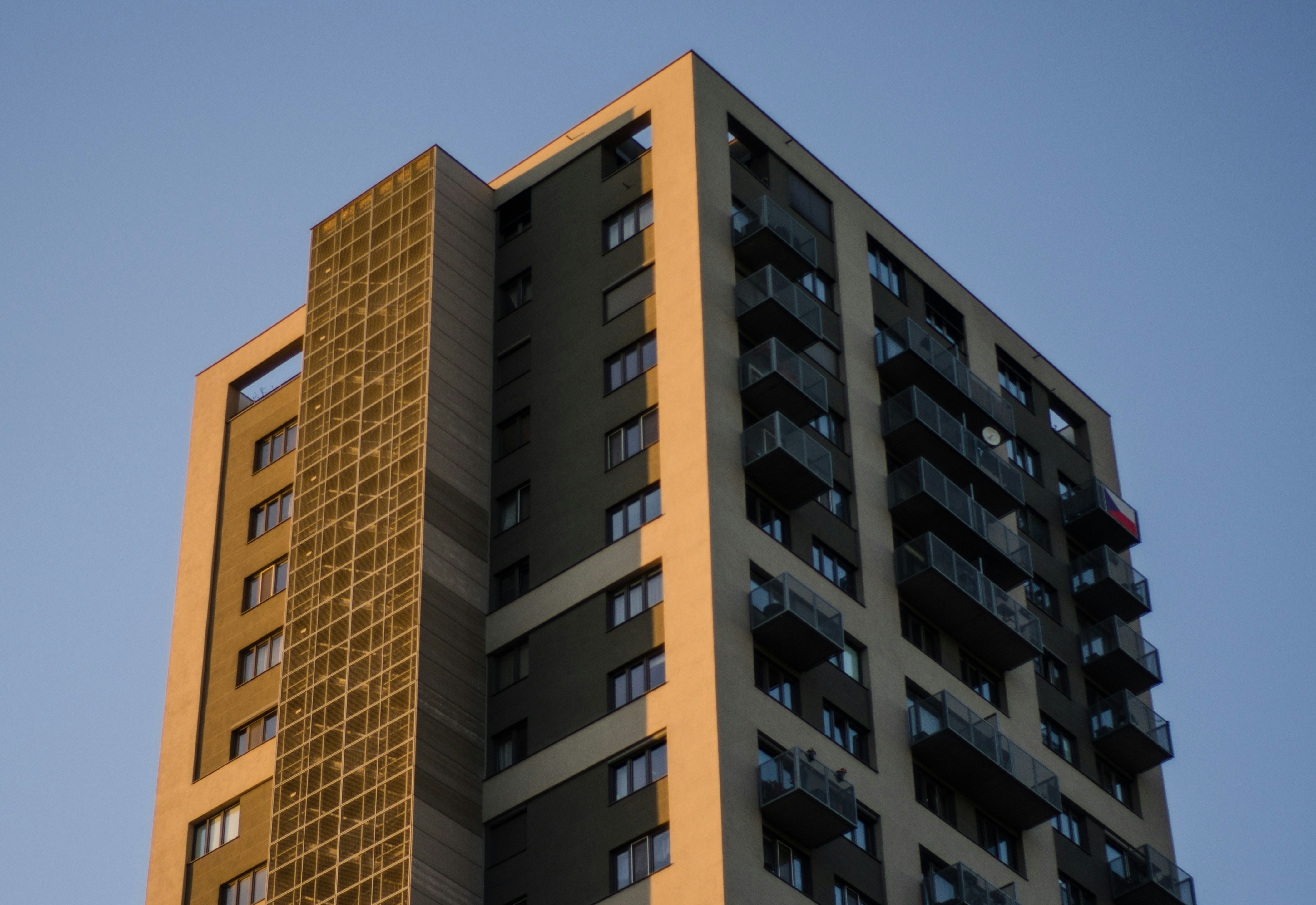 Tall building with multiple balconies against a clear blue sky, illuminated by warm evening light.