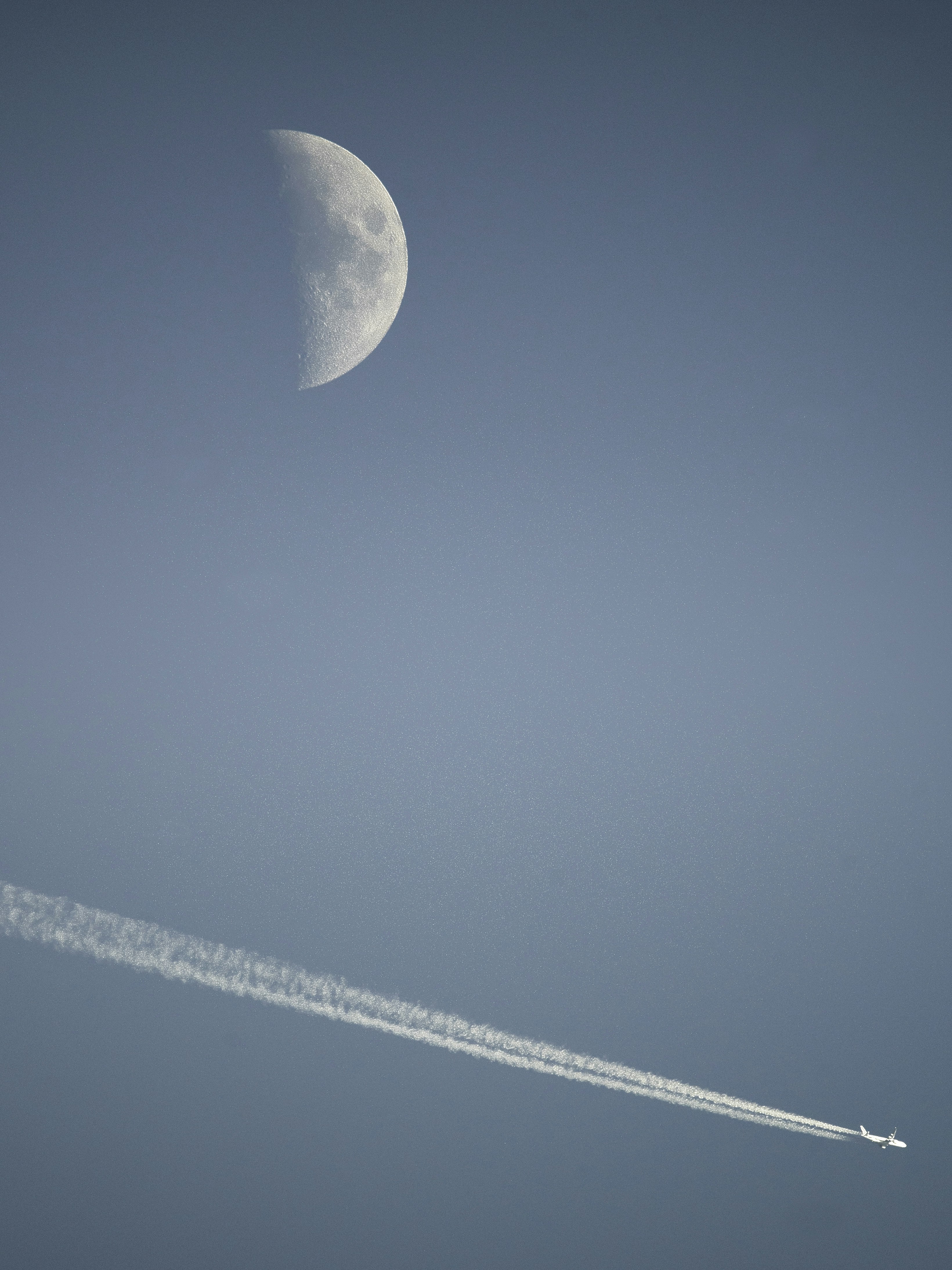 a plane flying in the sky with a half moon in the backgroundEmilio Garcia