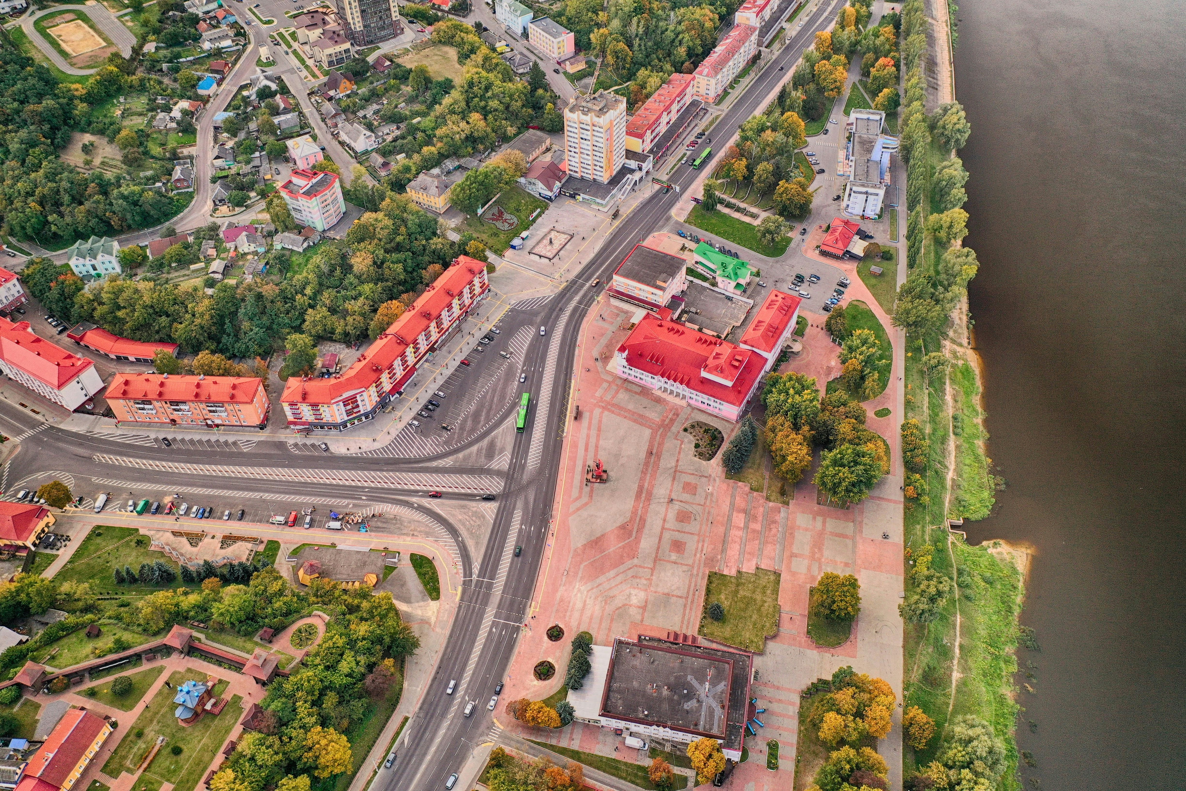 Aerial view showcasing a vibrant urban landscape along a riverbank, featuring residential buildings, a park, and a bustling roadway.