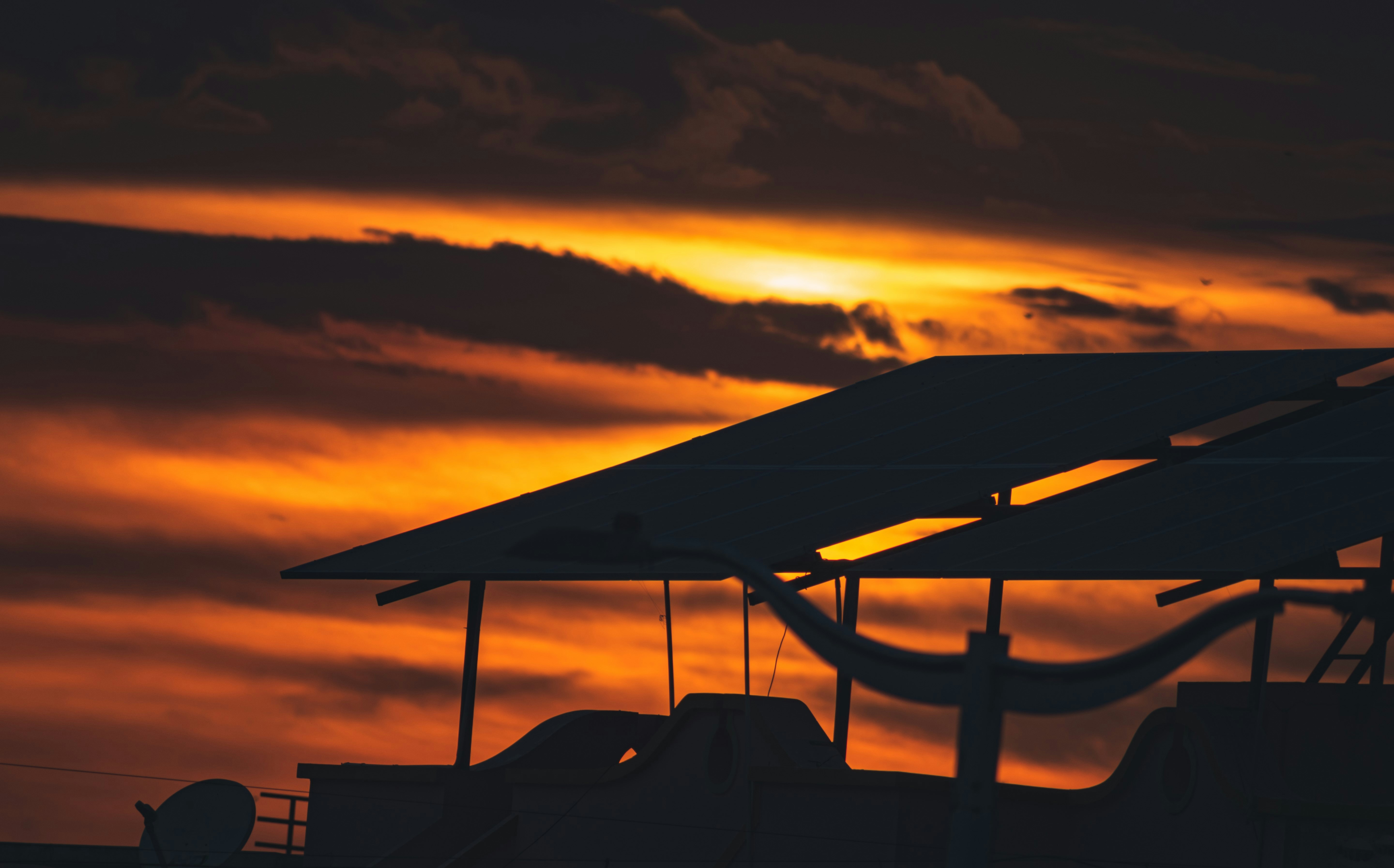 Silhouetted rooftops and structures against a vibrant orange sunset.