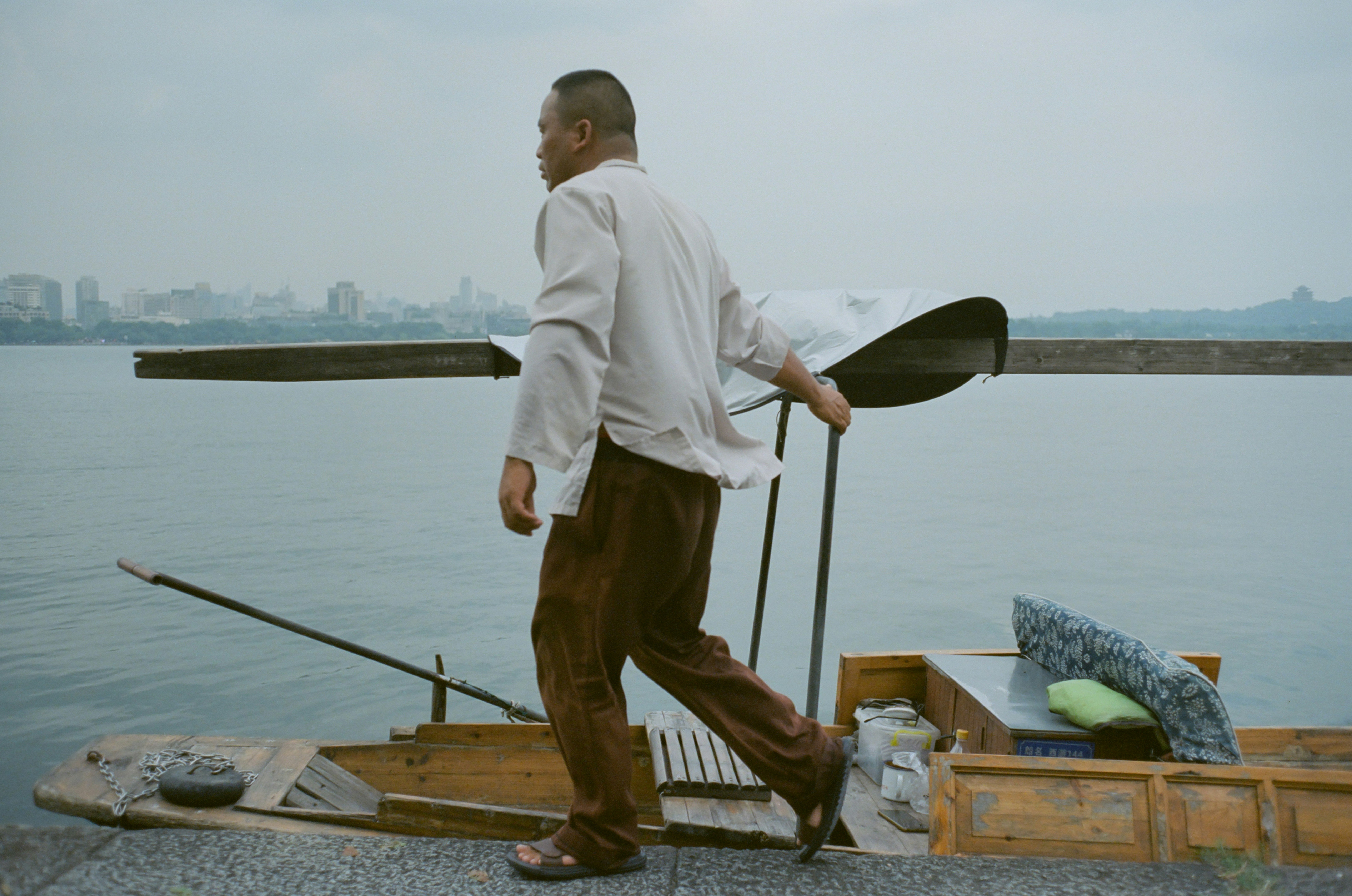A fisherman strides confidently along the dock, preparing his boat for a day on the water, with a city skyline faintly visible in the background.