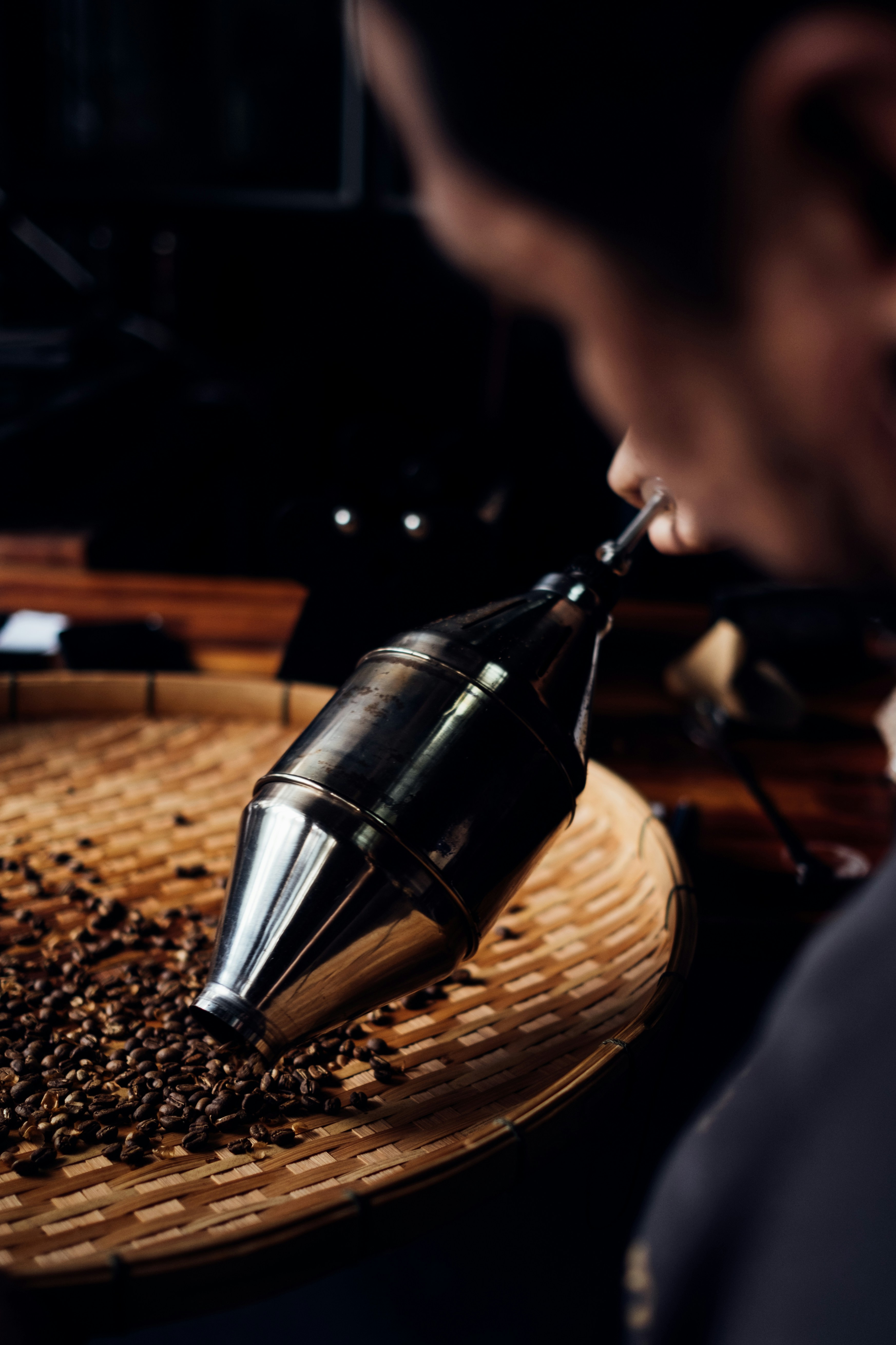 Person using a traditional coffee roaster to process beans on a woven tray.