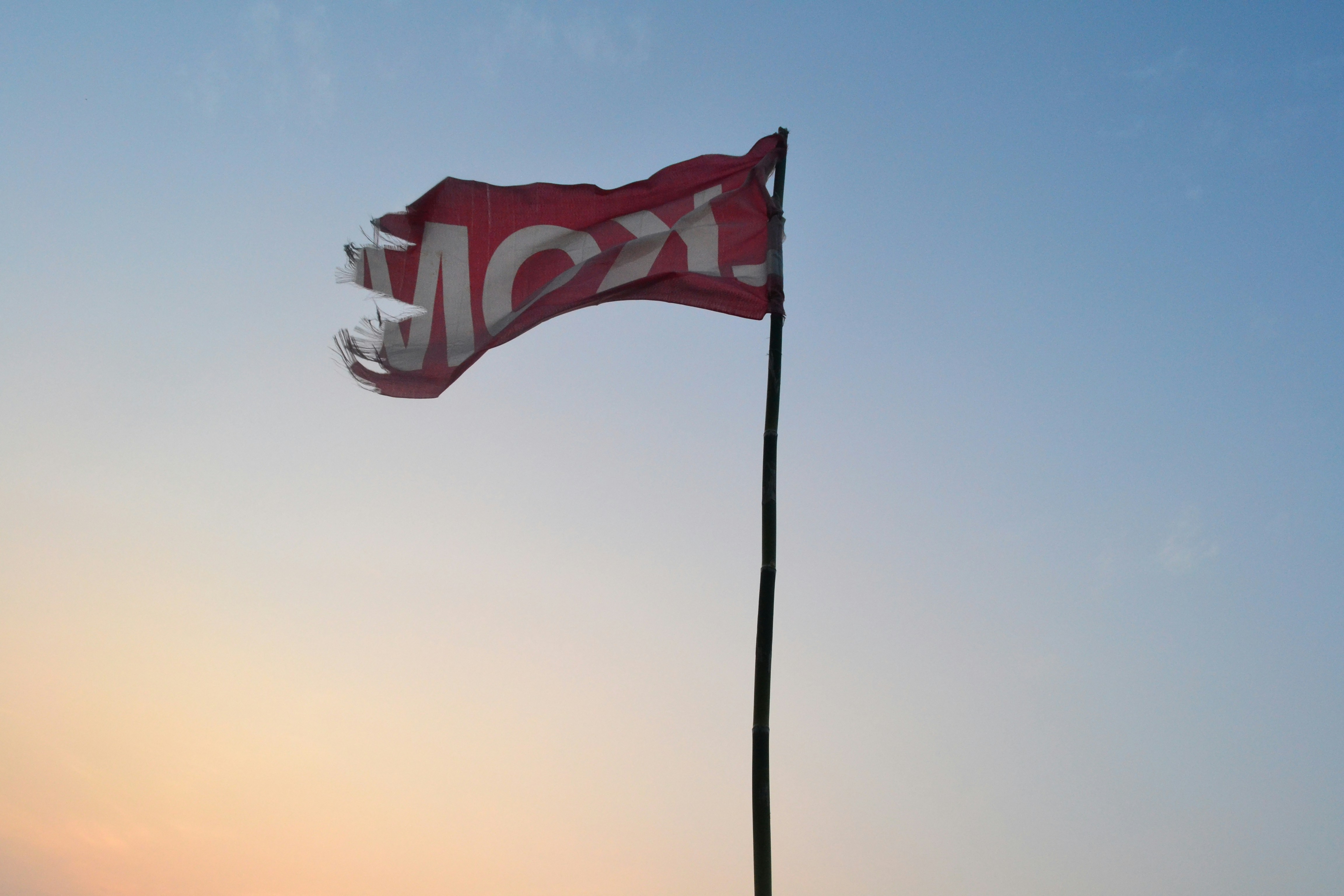 Tattered red flag waving atop a pole against a gradient sky at dusk.