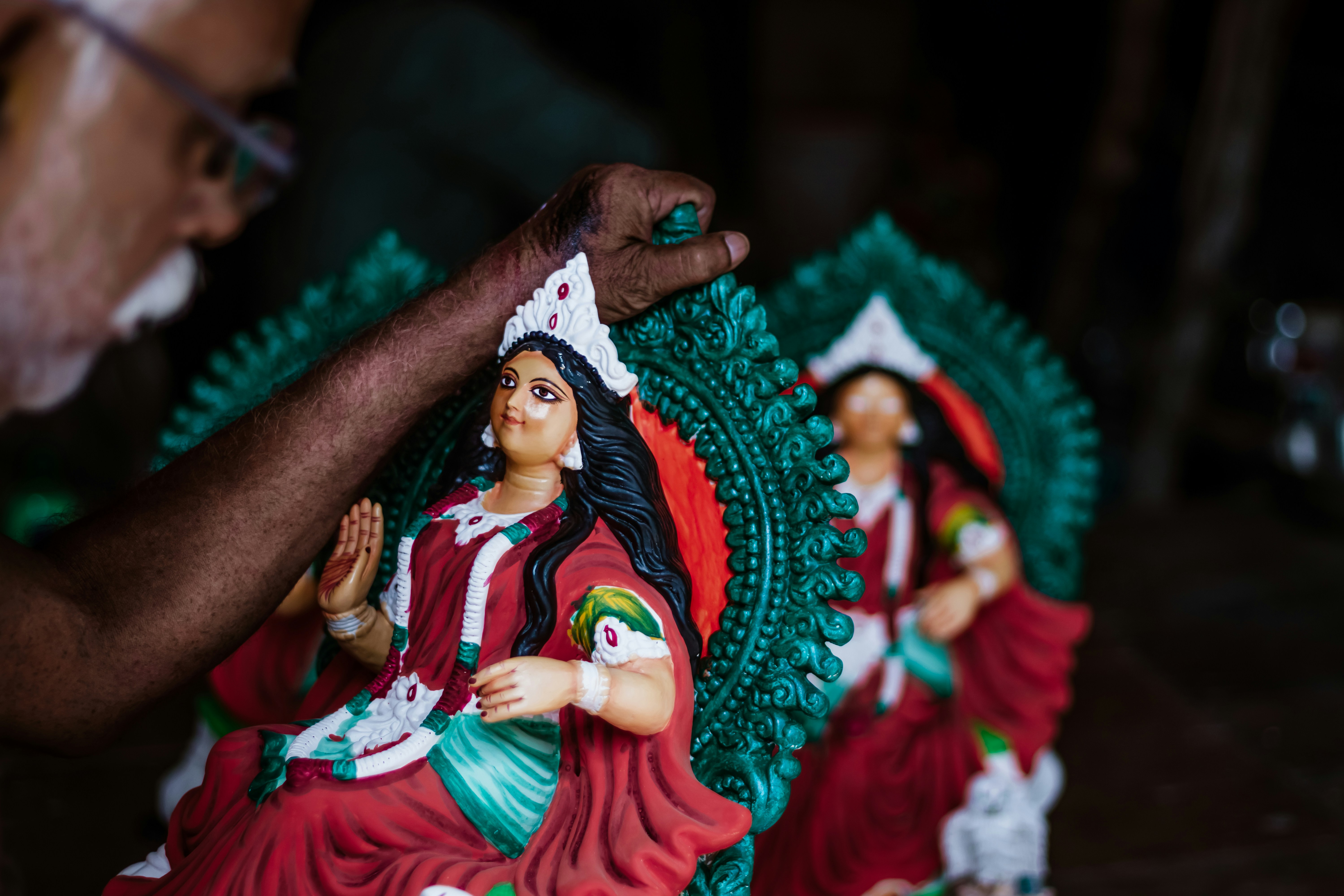 Artisan meticulously detailing a colorful idol of a goddess, showcasing traditional craftsmanship in a workshop setting.
