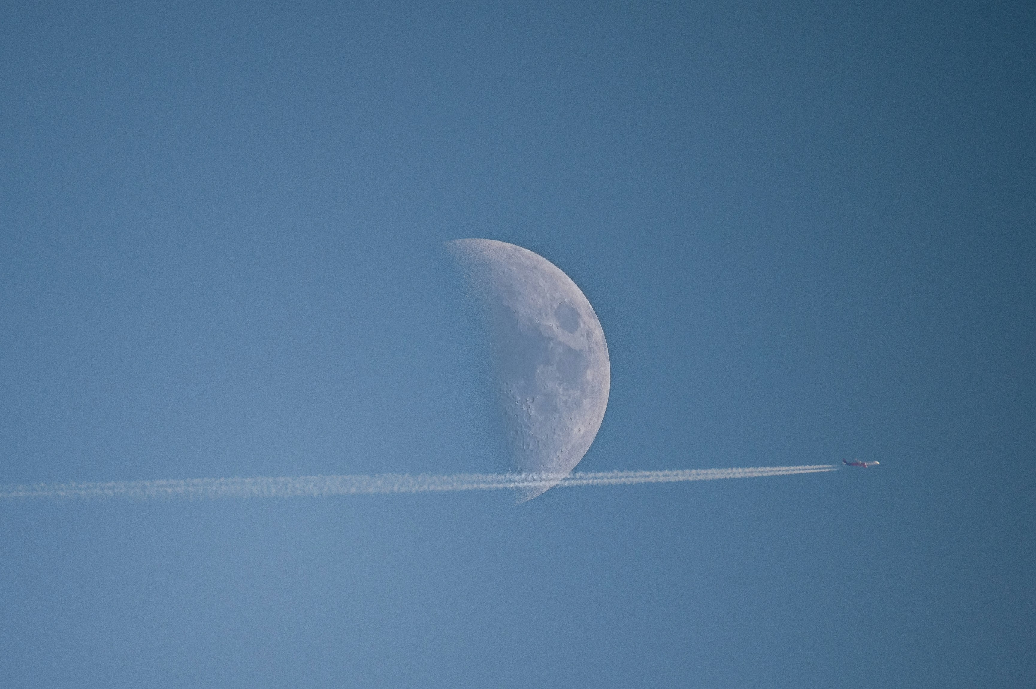 Luna in the Clear: Jet Trail Across a Pale Blue Sky