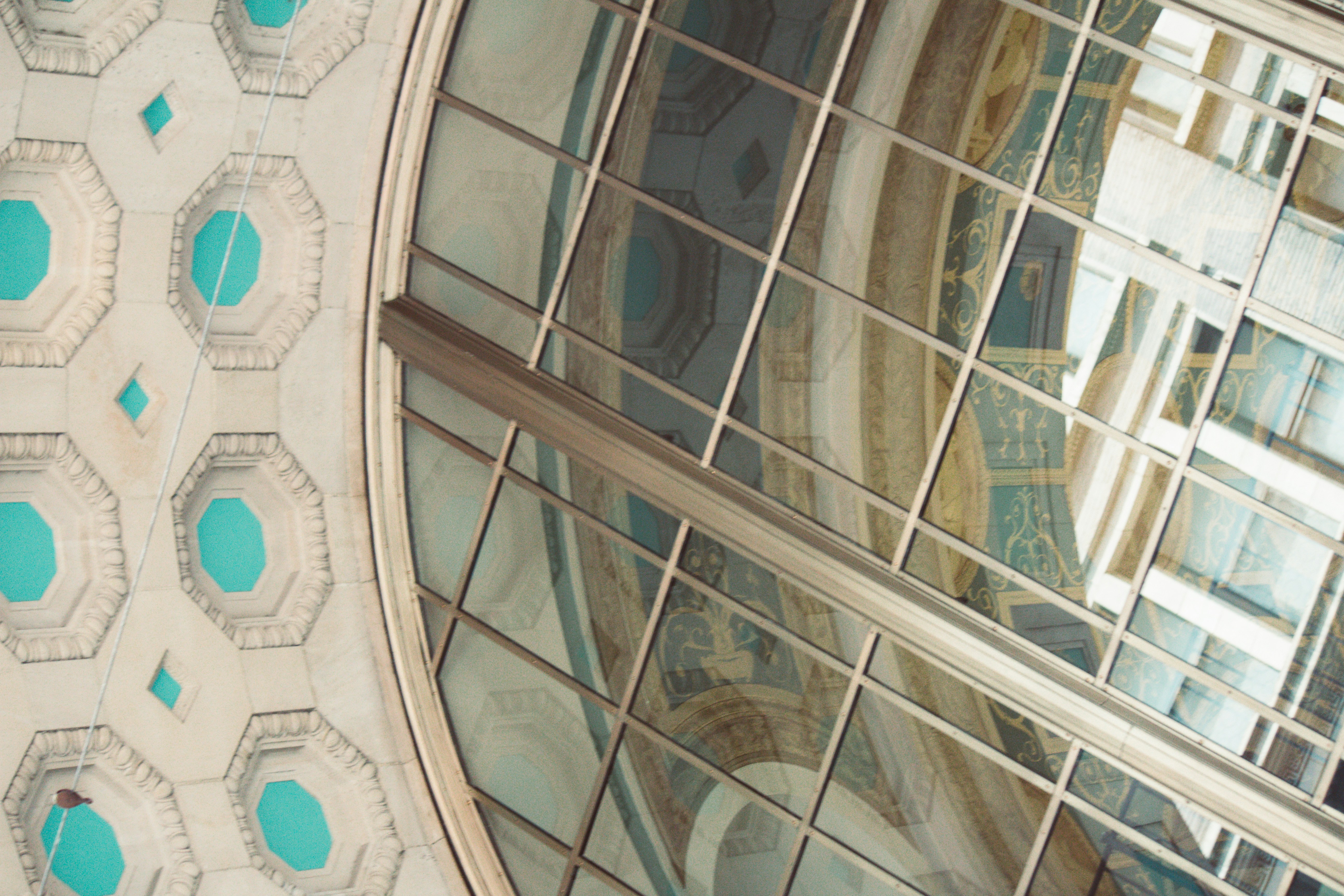 Intricate ceiling design reflected in a glass facade with teal accents.