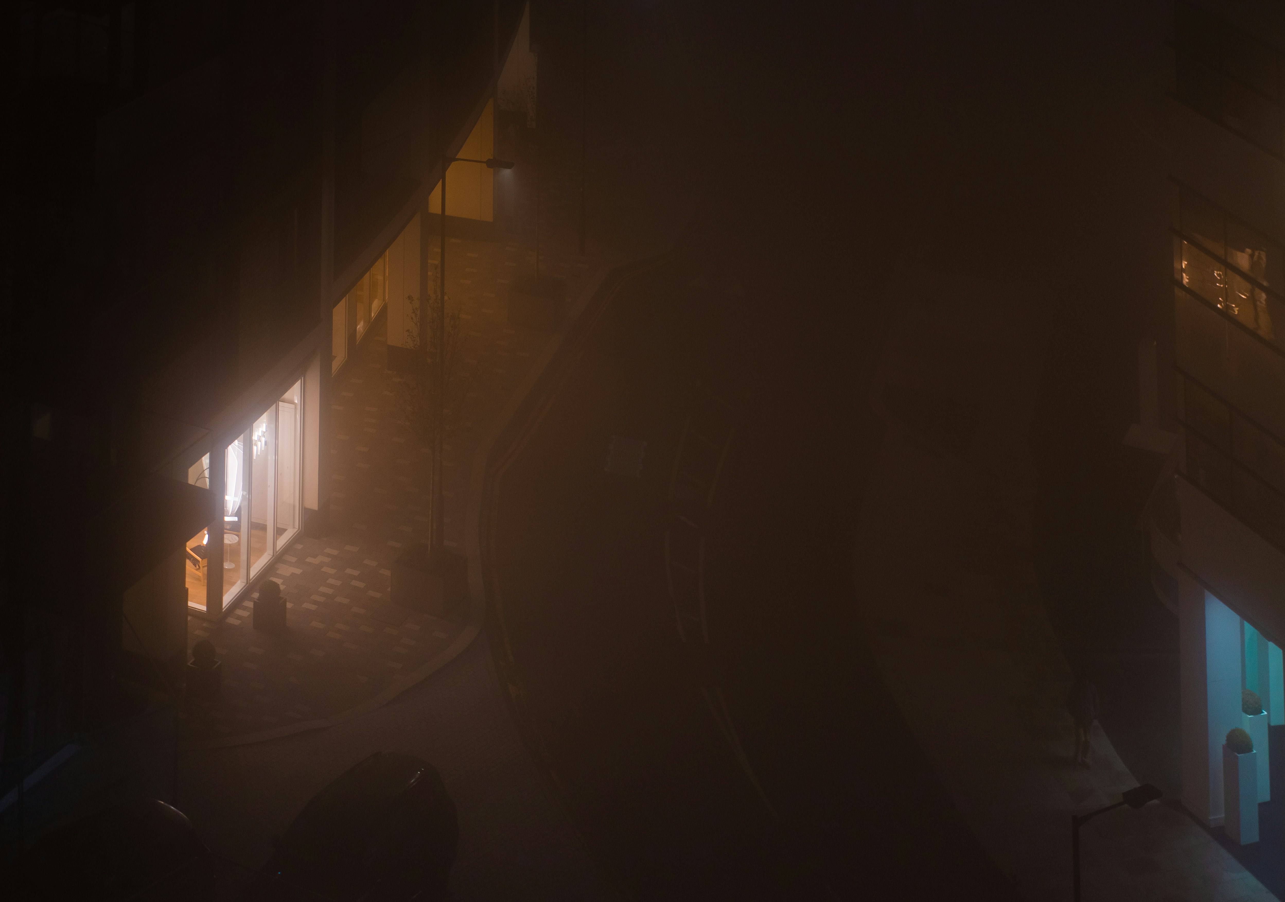 Dimly lit street with fog, illuminated by warm light from a nearby window.