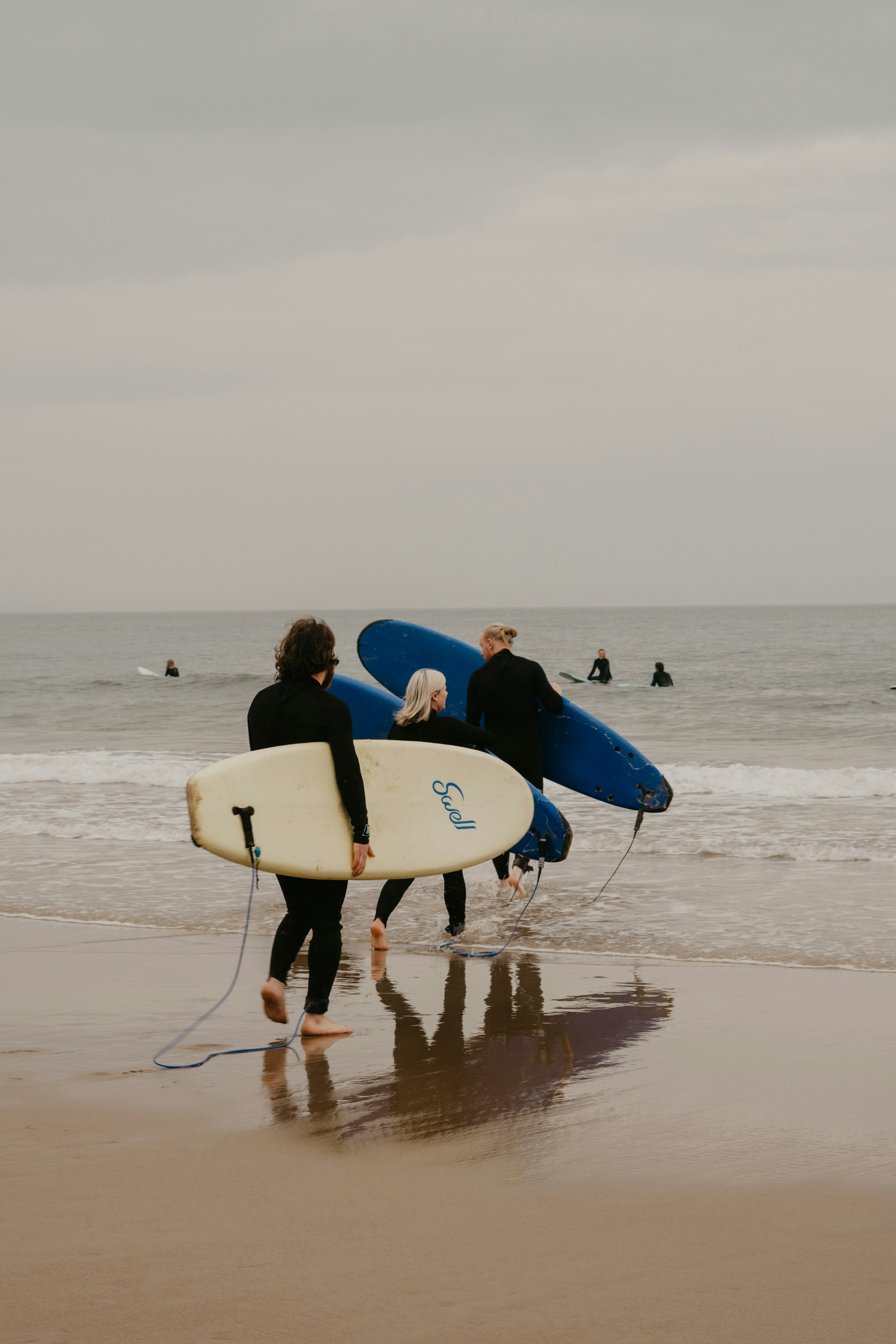 Surfers walking along the shore, carrying surfboards towards the ocean under a cloudy sky. The scene captures the essence of beach culture and anticipation.