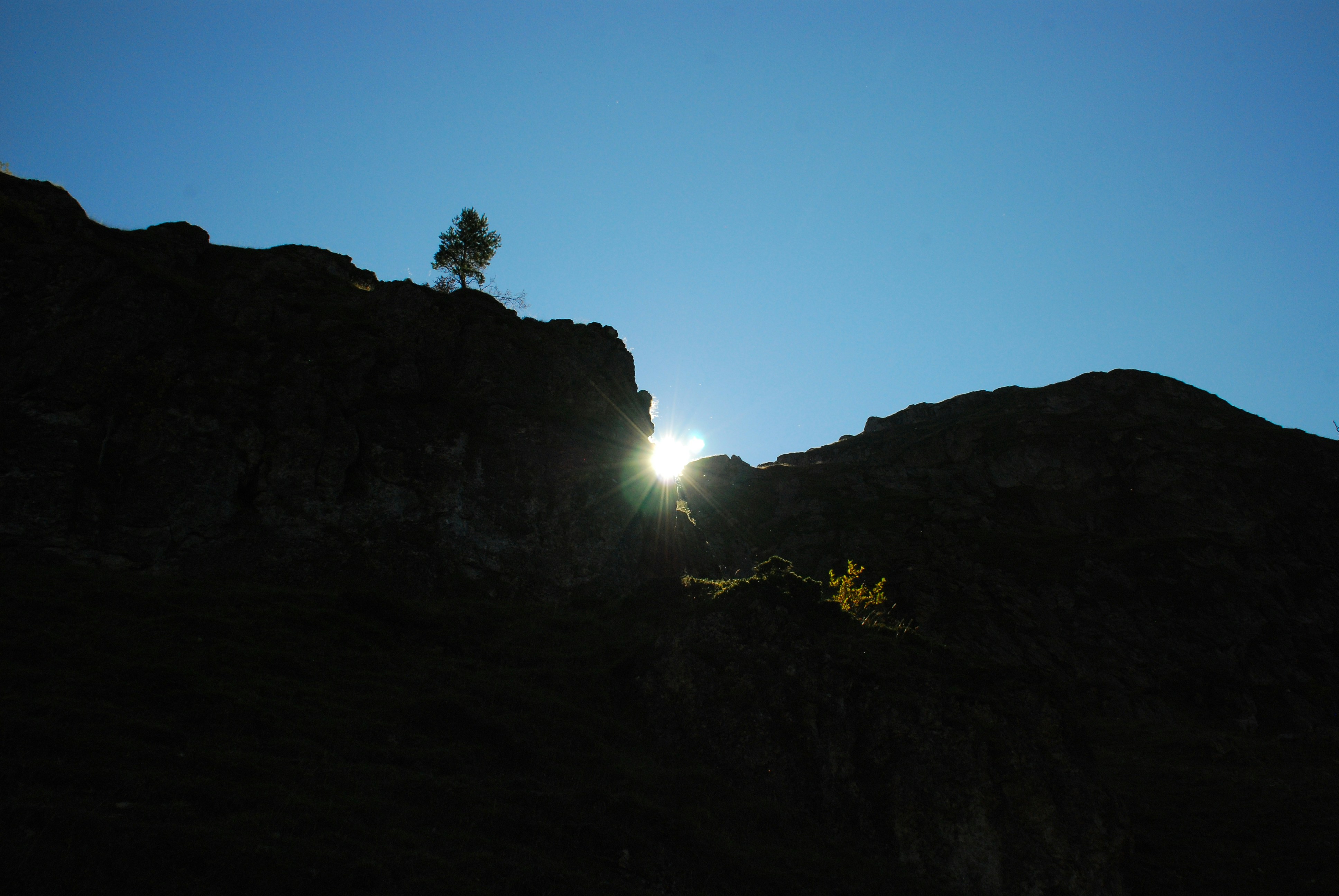 The sun shines brightly through the shadow of a mountain photo – Free ...