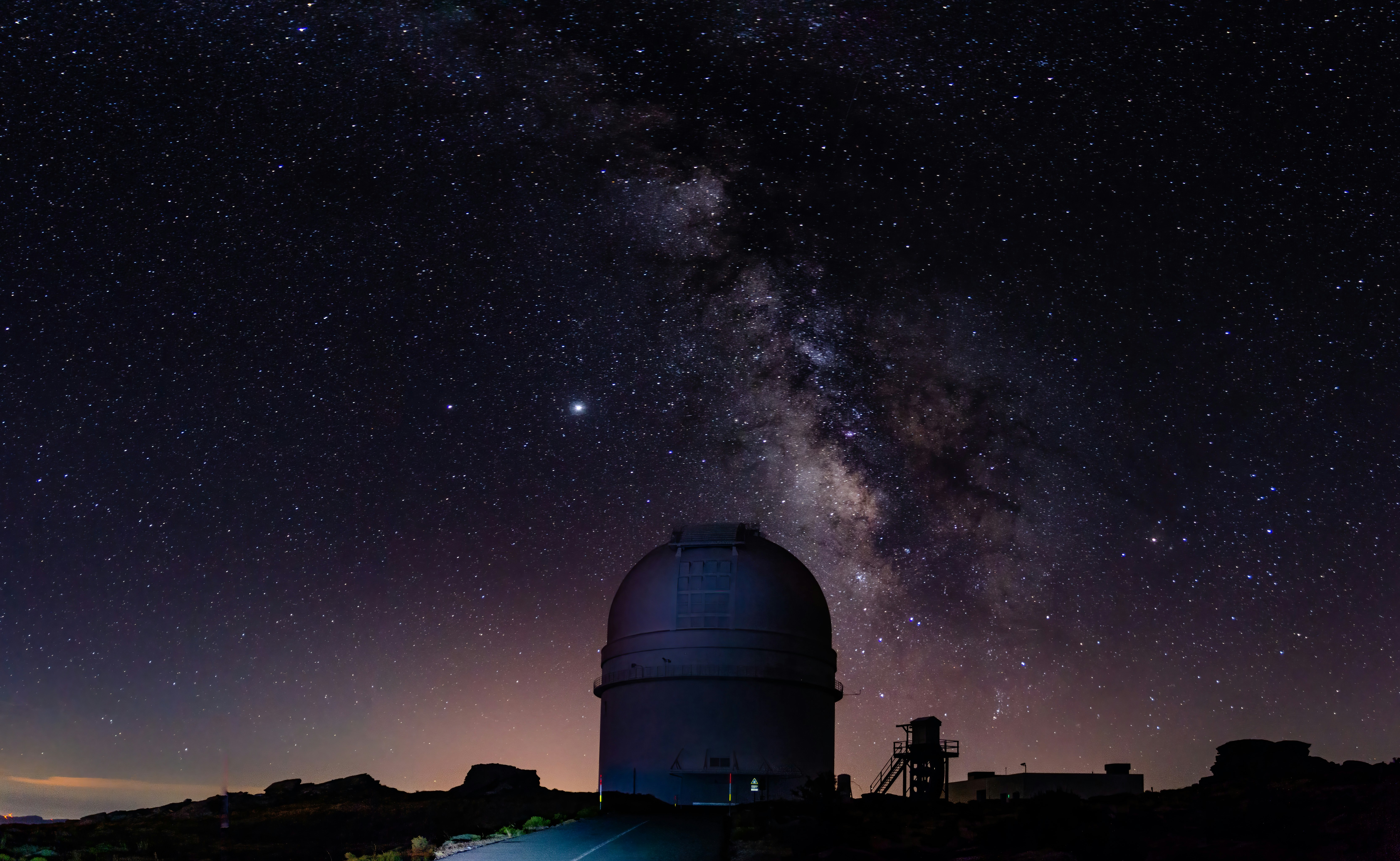 A large telescope on top of a hill under a night sky filled with stars ...