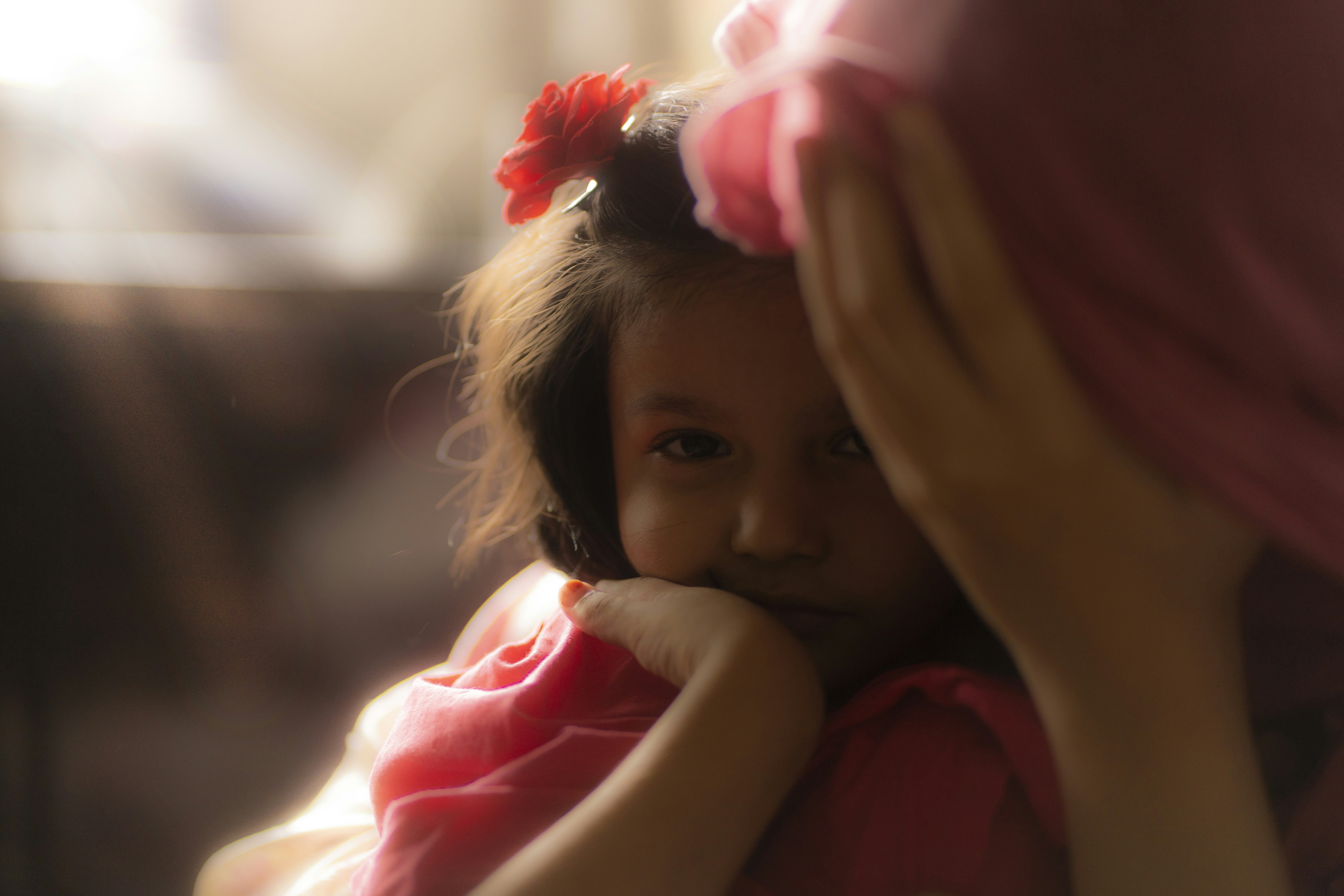 Child peeks shyly from behind a caregiver's embrace in soft, warm lighting.