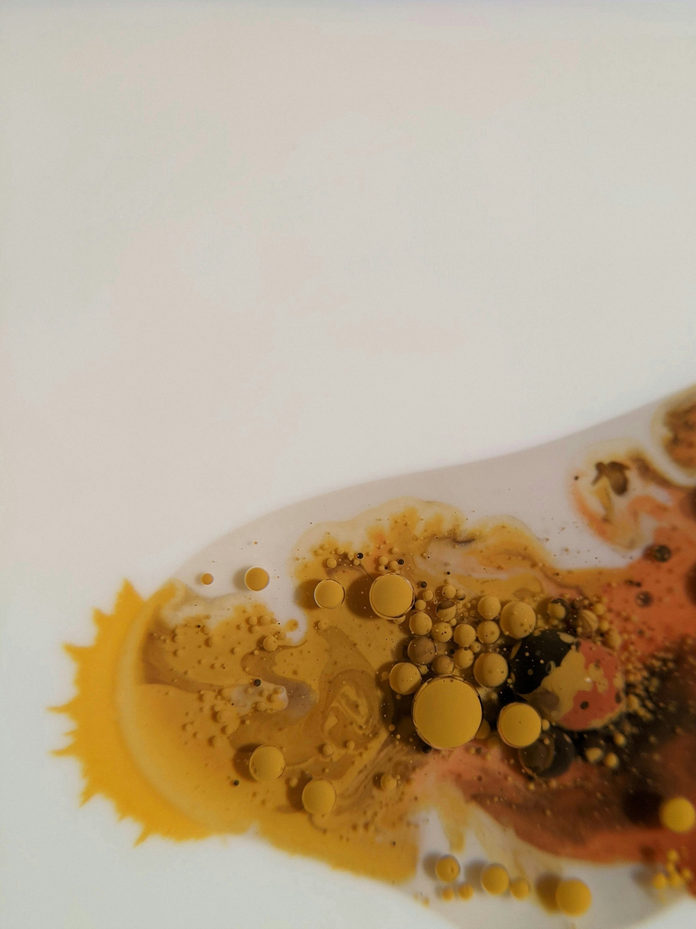 Abstract composition featuring vibrant yellow and orange droplets merging on a white background. The interplay of colors creates a dynamic visual flow.