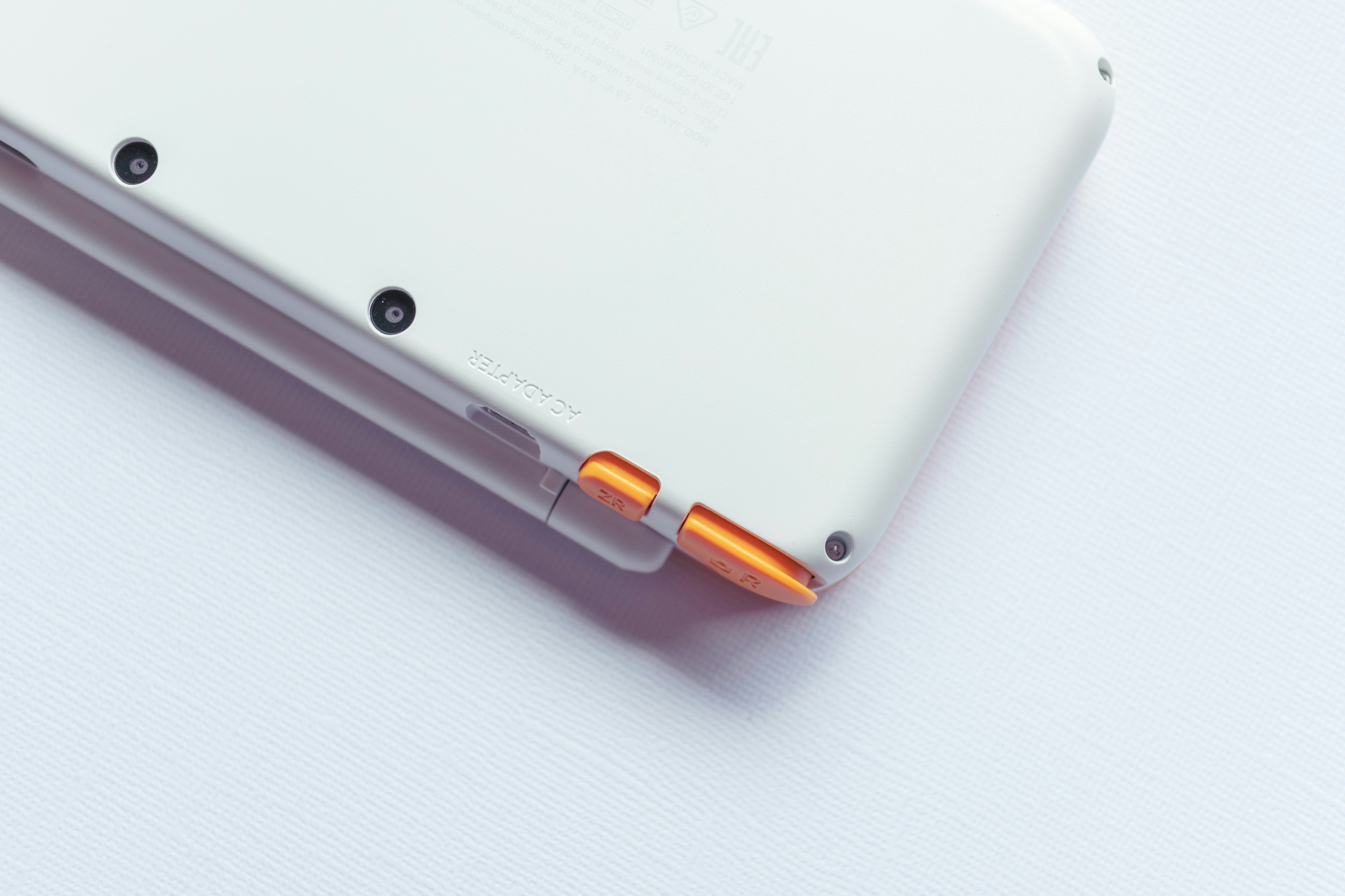 Close-up of a white handheld gaming device featuring vibrant orange buttons against a textured background.