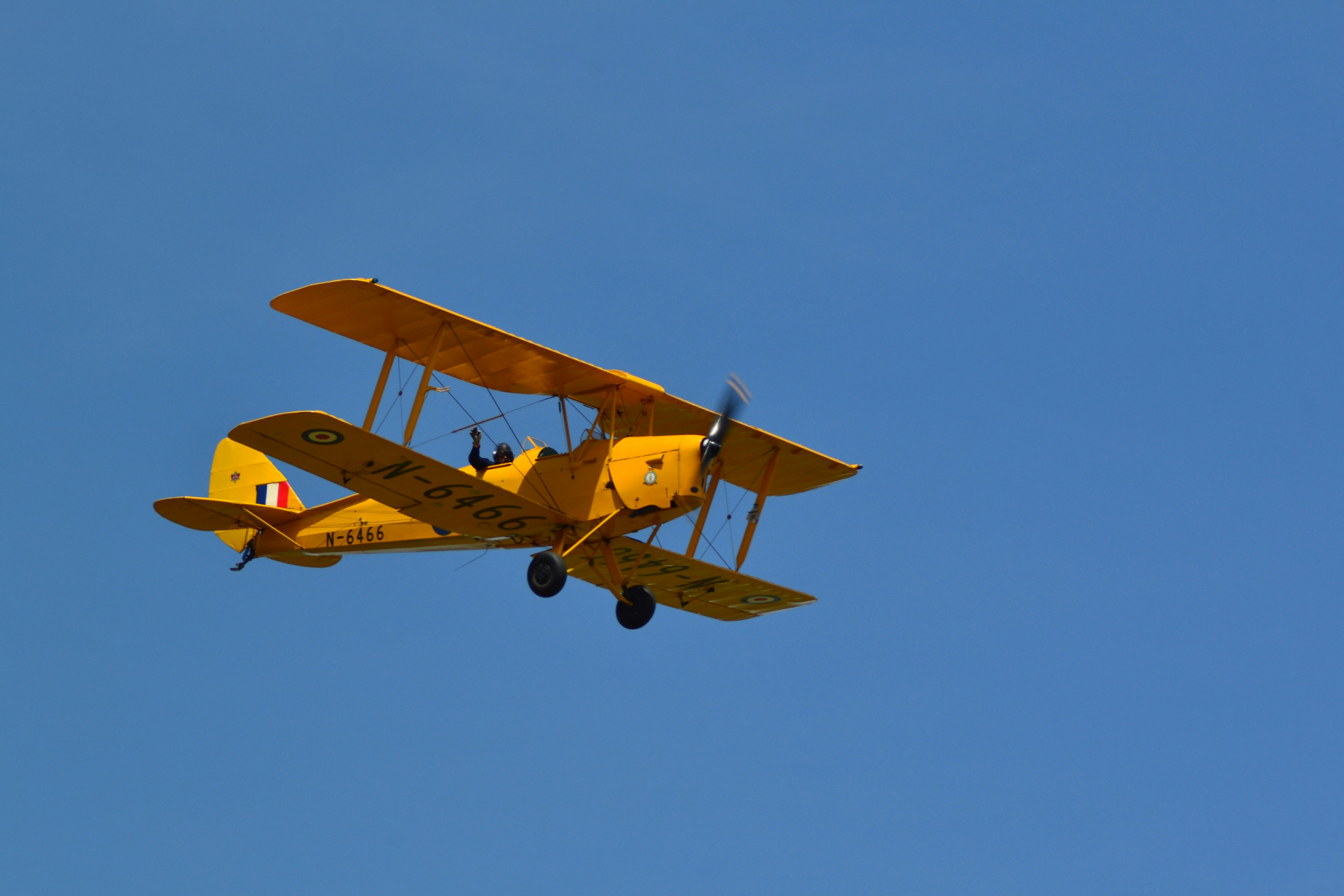 Bright yellow biplane soaring through a clear blue sky, showcasing its vintage design and vibrant colors.