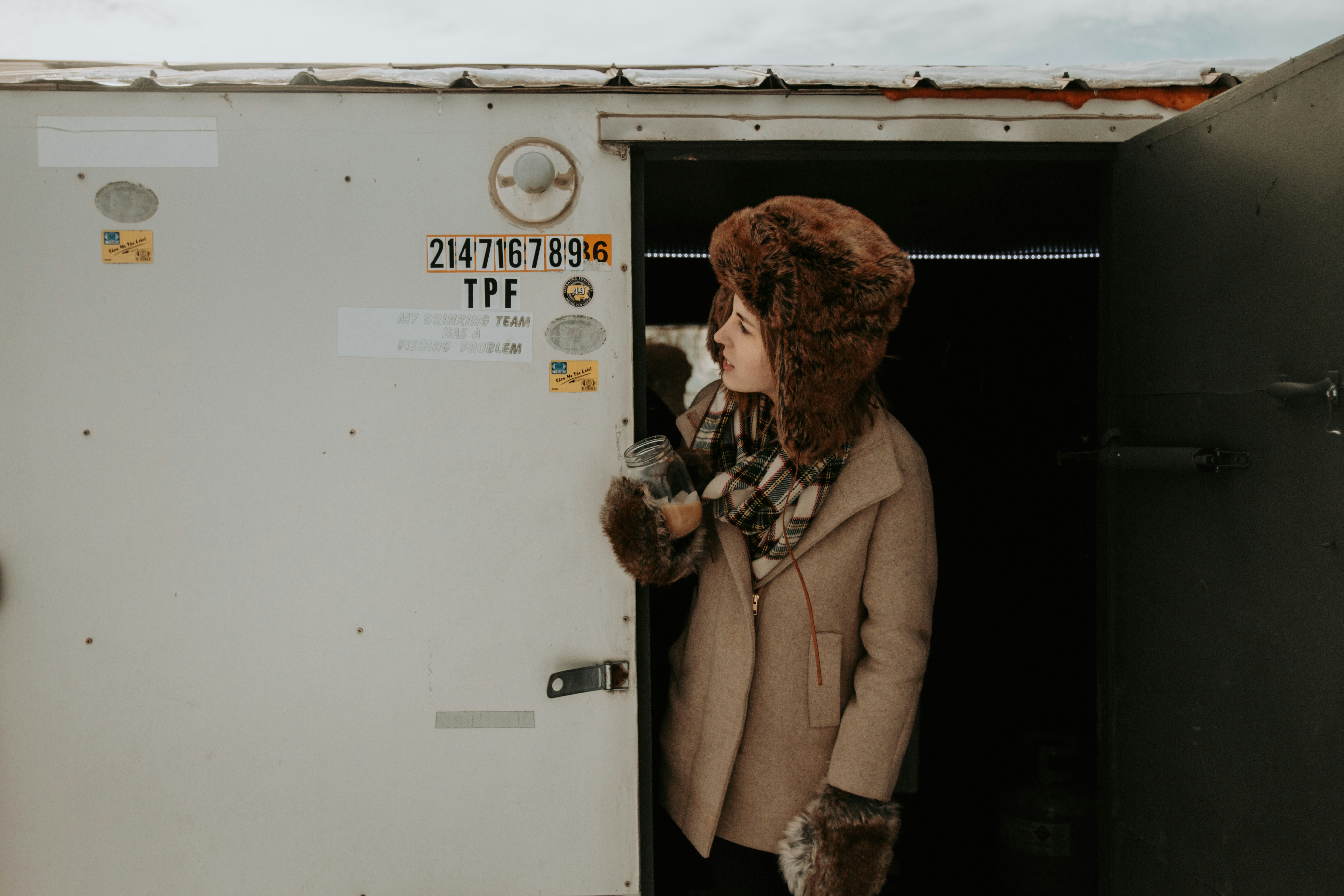 Person in warm clothing stands by an industrial container, peering thoughtfully into the distance.