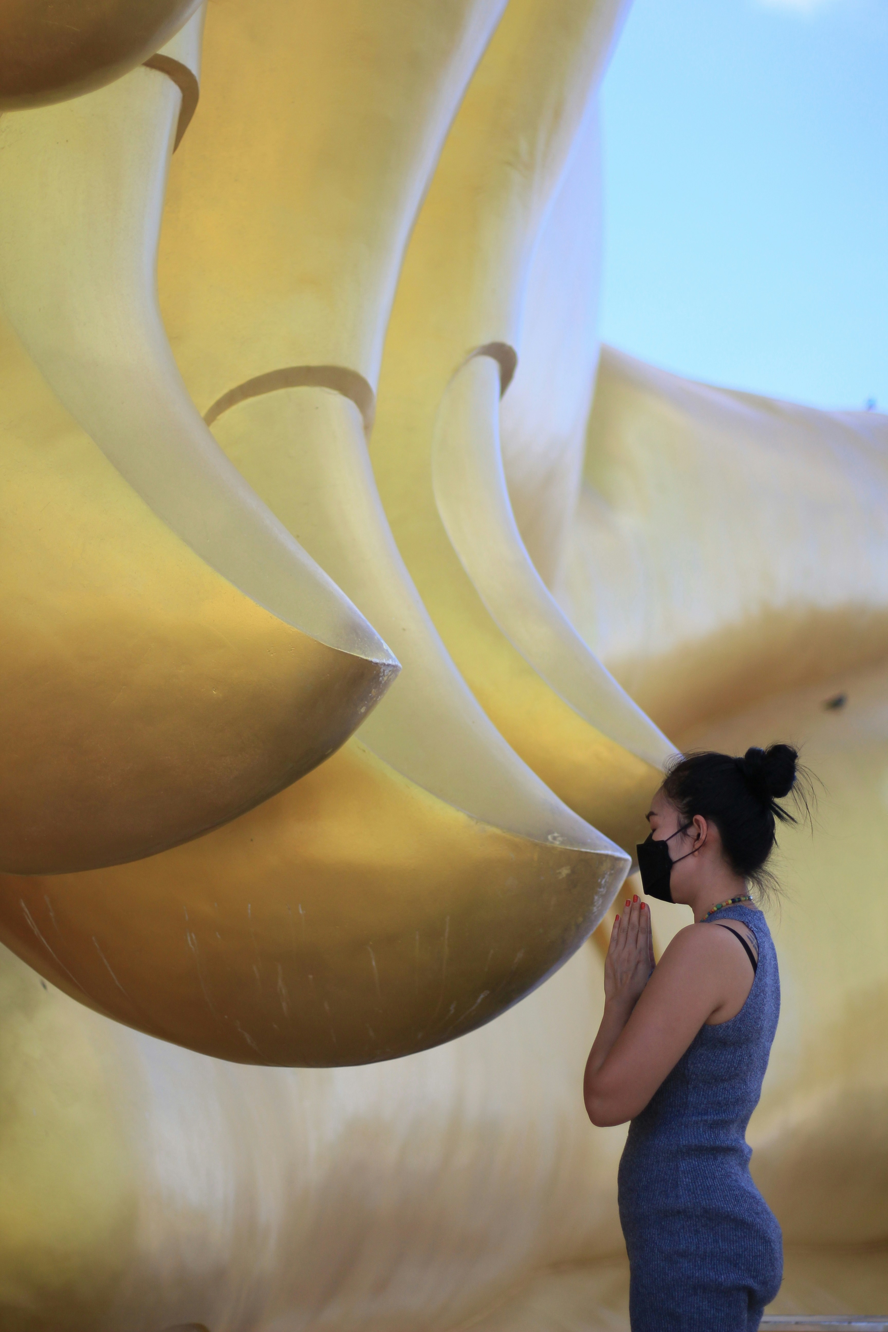 Woman in prayer stance before a large golden sculpture, embodying tranquility and devotion. The sculpture’s intricate details emphasize its spiritual significance.