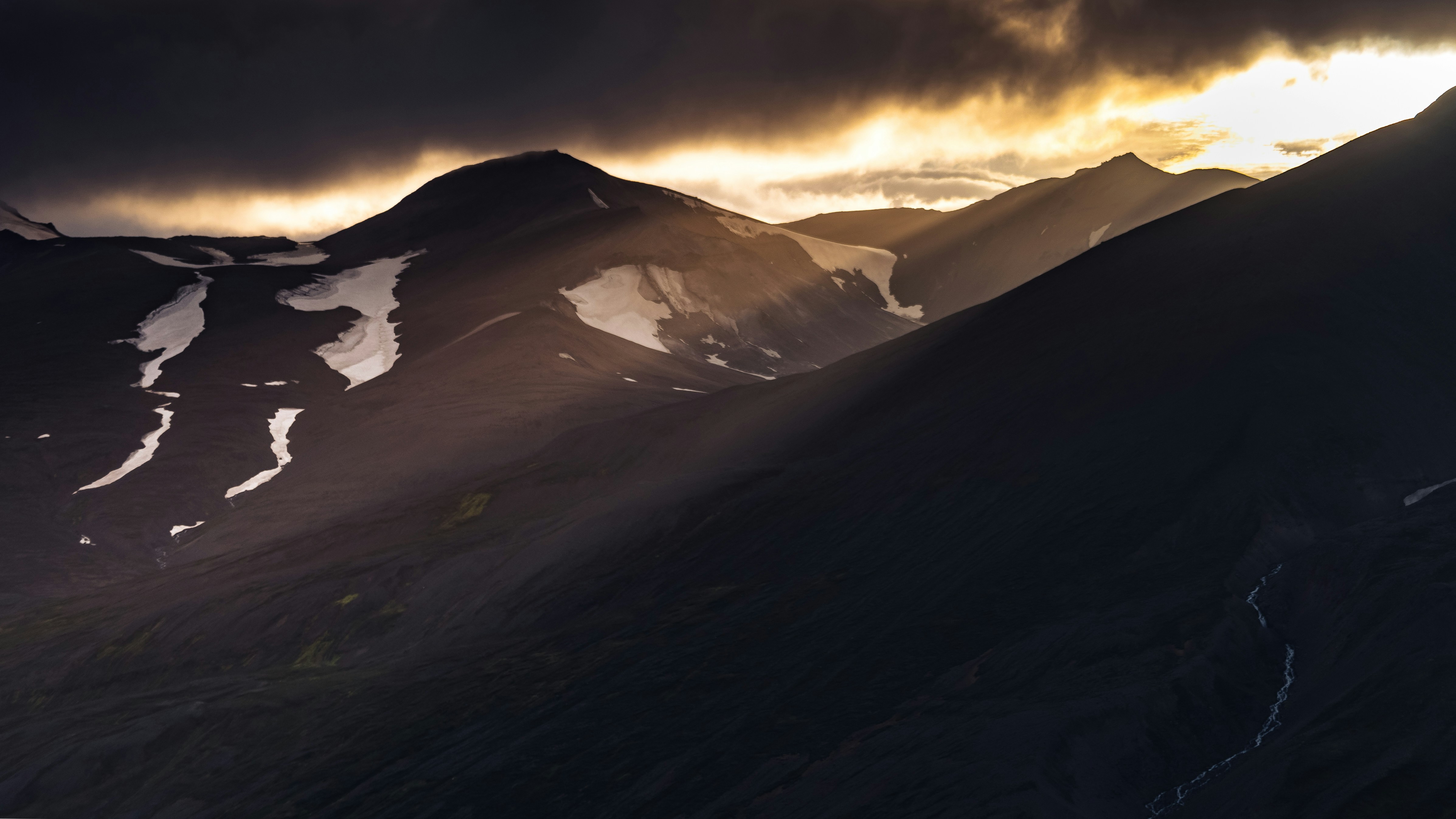 Dramatic mountain landscape with shadows and light interplay, highlighting snow-capped ridges and deep valleys.