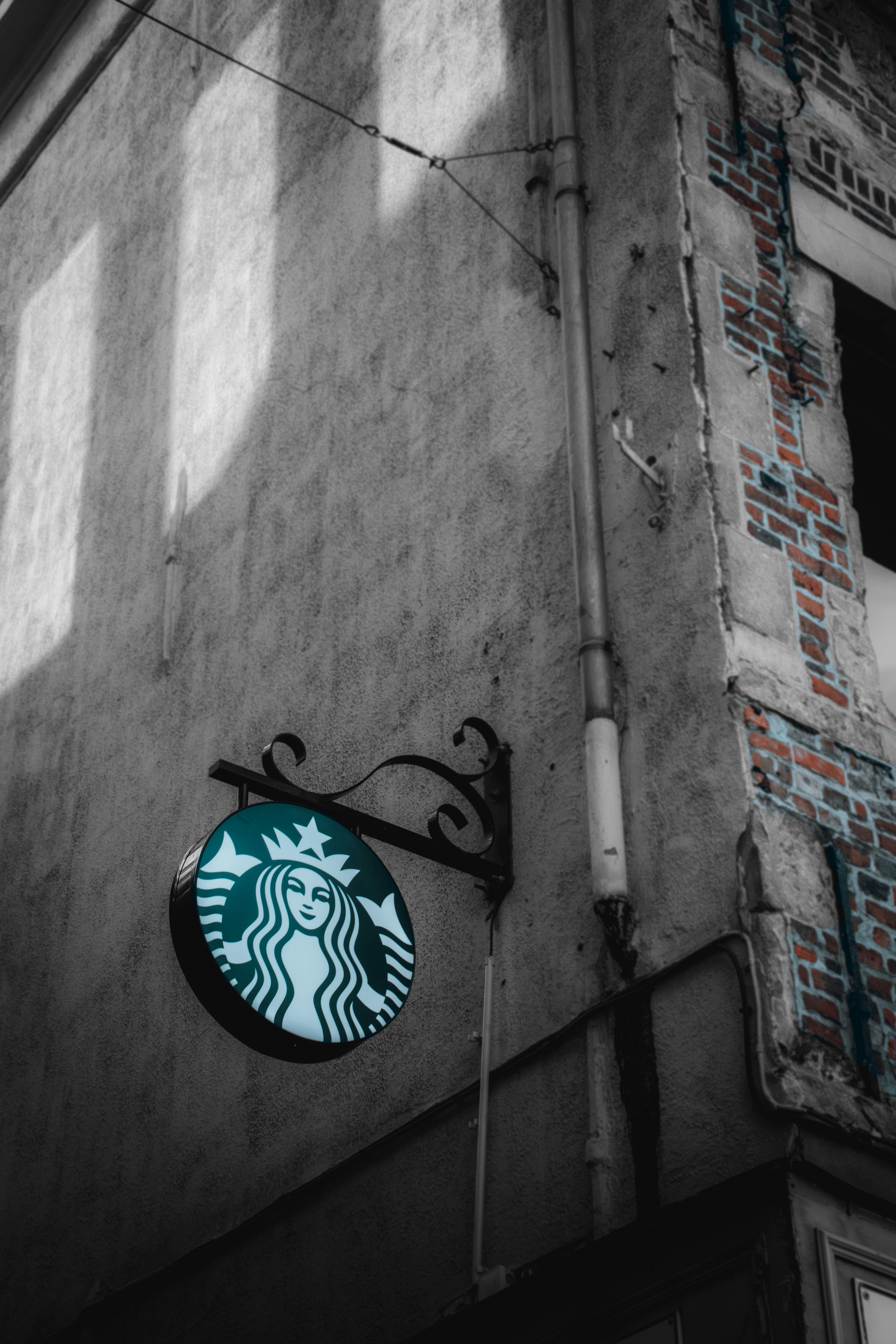 Illuminated Starbucks logo hanging on a textured wall, contrasting with the surrounding shadows.