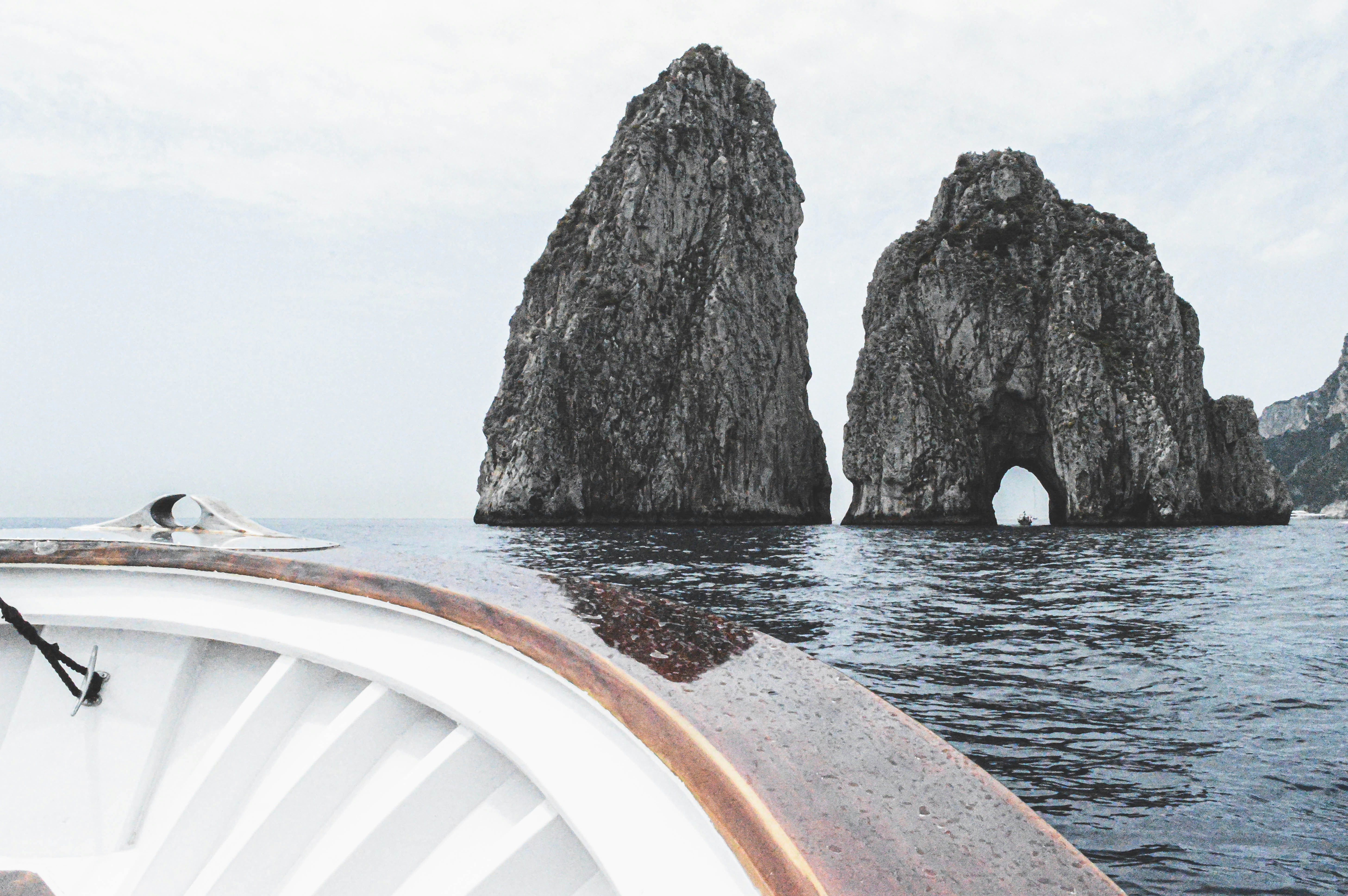 A boat traveling past two large rocks in the ocean photo – Free Italy ...