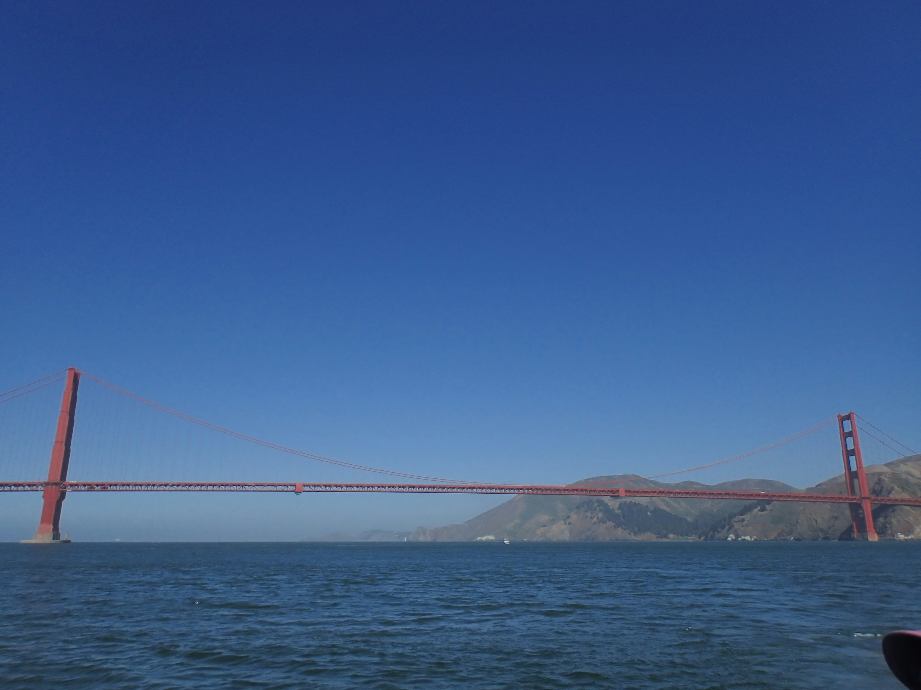 Golden Gate Bridge spans the bay, its red towers slicing across the deep blue water. A cloudless sky completes the crisp coastal scene.
