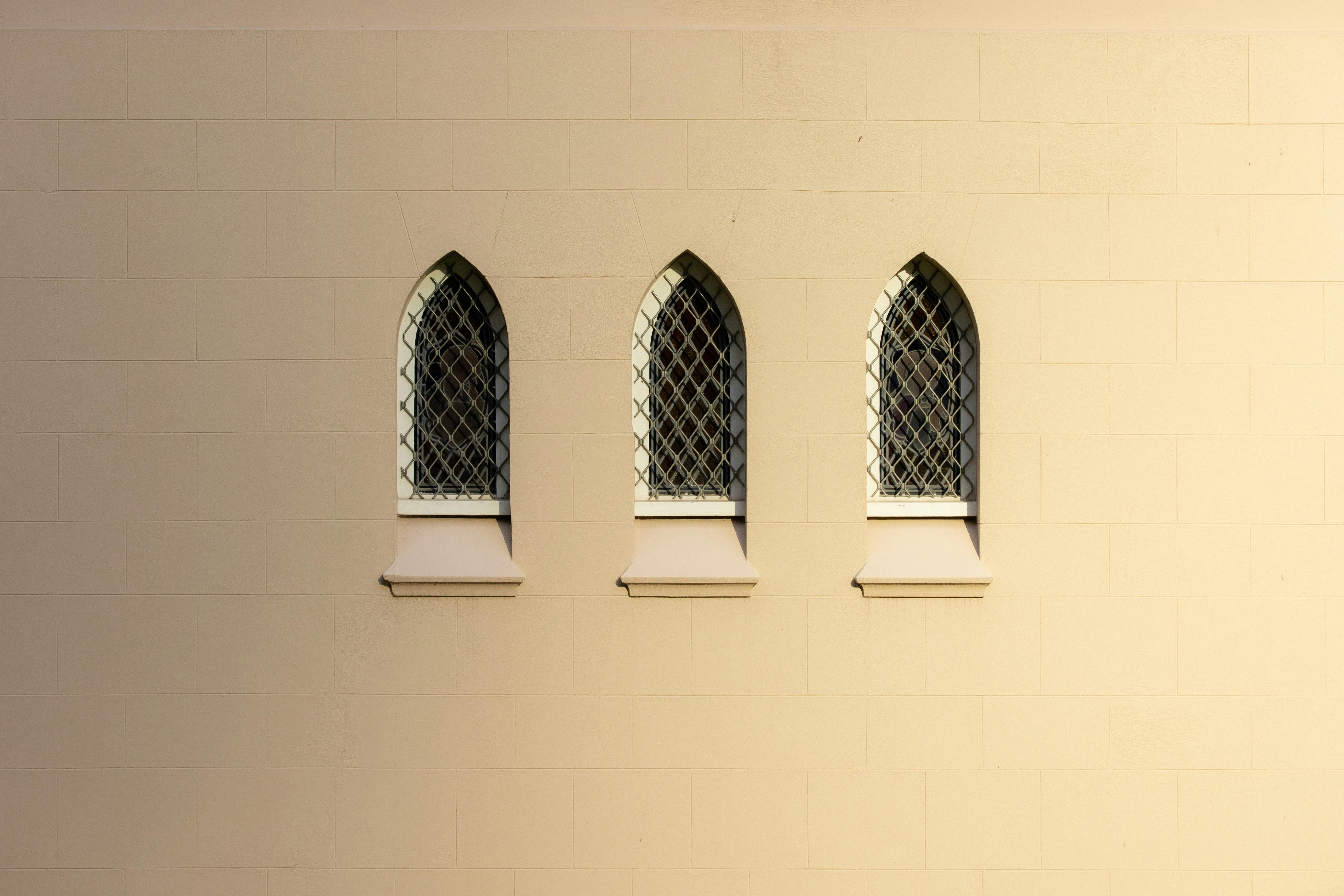 Three arched windows with intricate latticework, casting soft shadows on a pale wall.