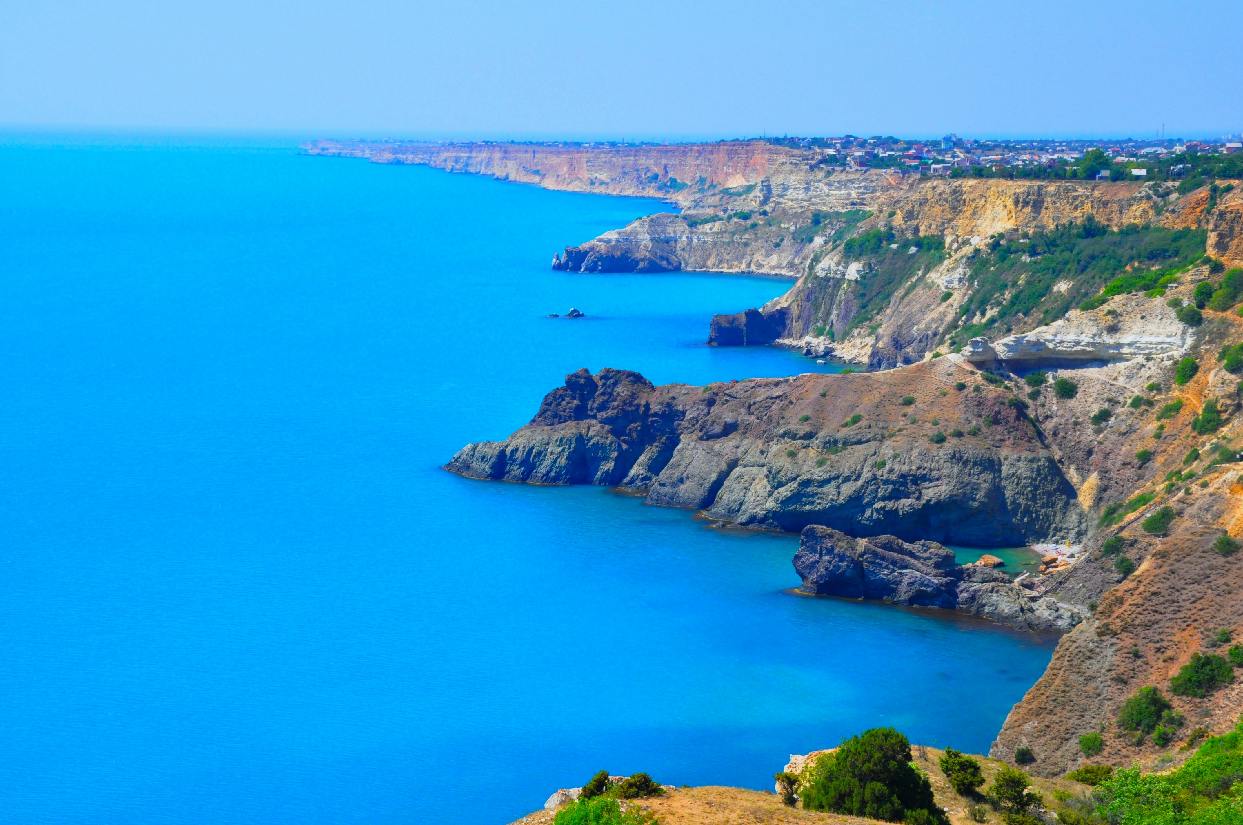 Vibrant coastal cliffs meeting a tranquil blue sea under a clear sky, showcasing the beauty of nature's palette.