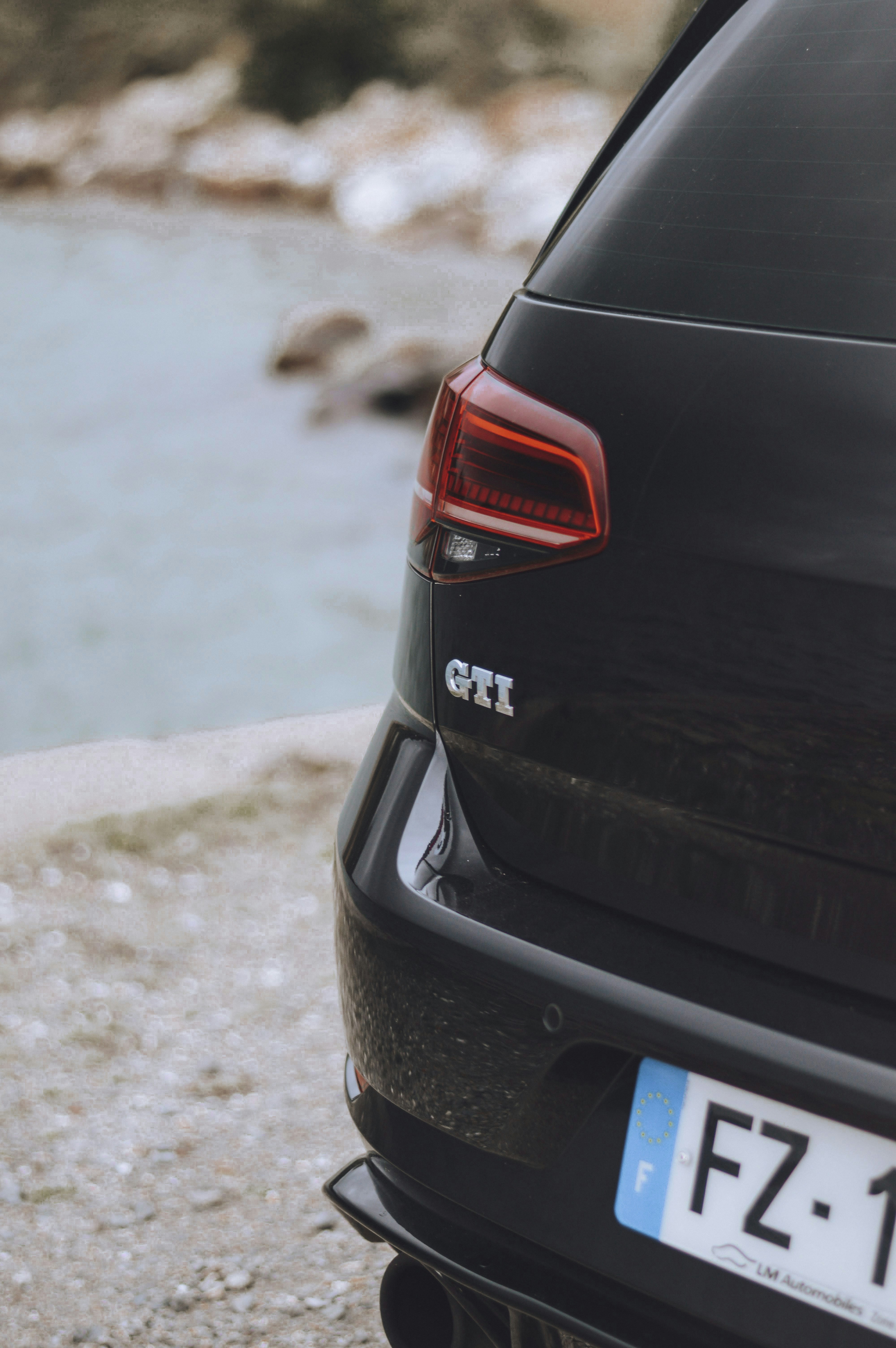 Close-up of a black GTI car's rear badge against a blurred natural backdrop. The image captures the sleek design and sporty character of the vehicle.