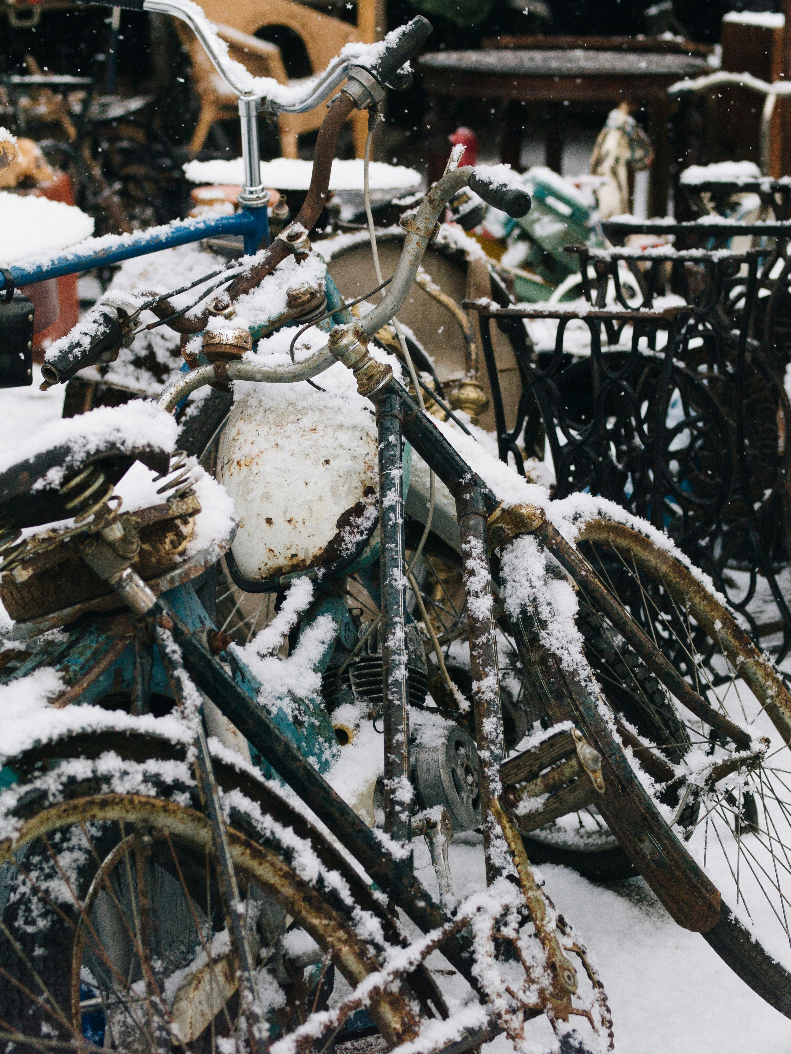 Snow-covered bicycles lean and tangle in a cluttered courtyard, their rusted frames and frost telling a story of neglect.