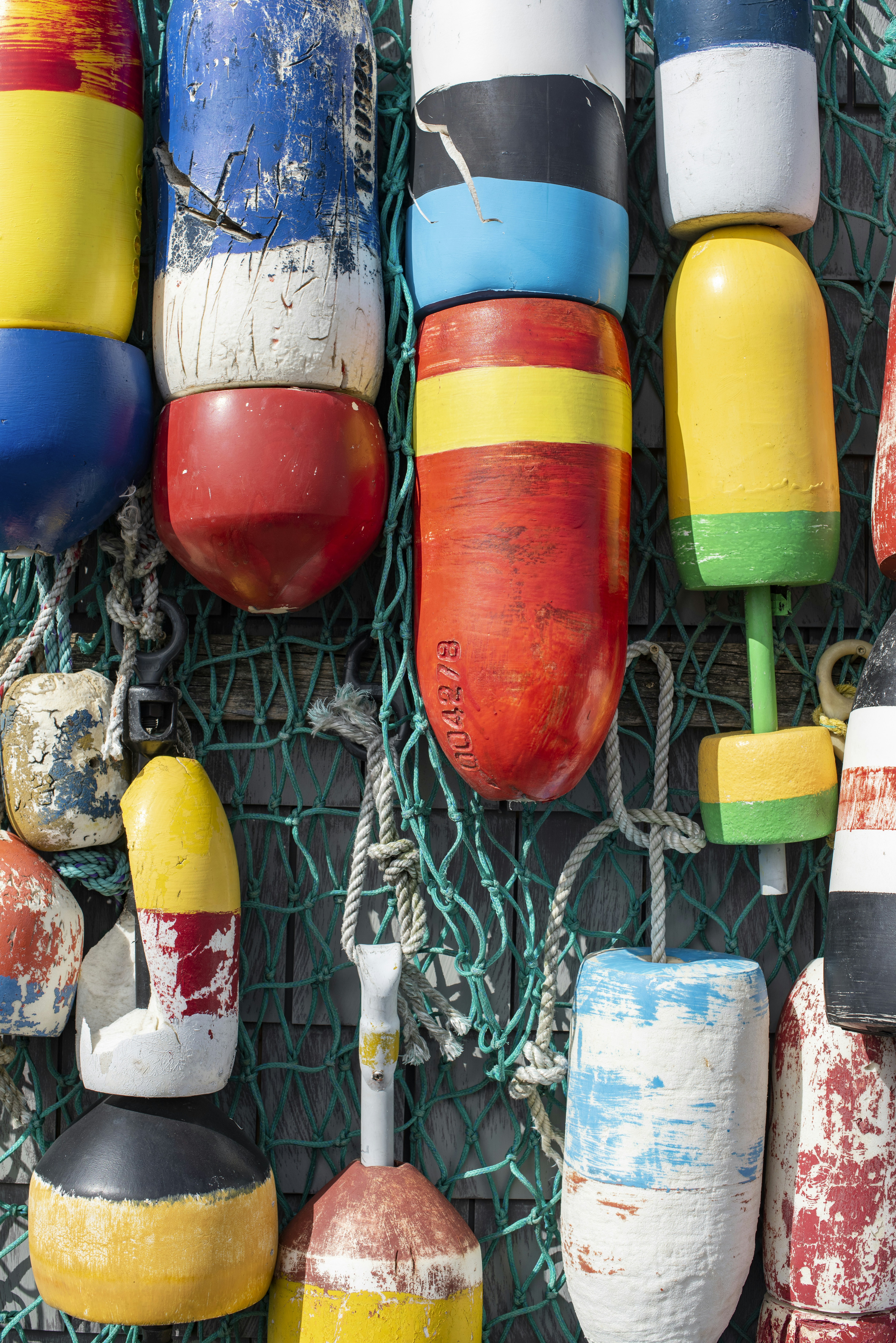 A vibrant collection of fishing buoys arranged against a green netting backdrop, showcasing a variety of colors and textures.