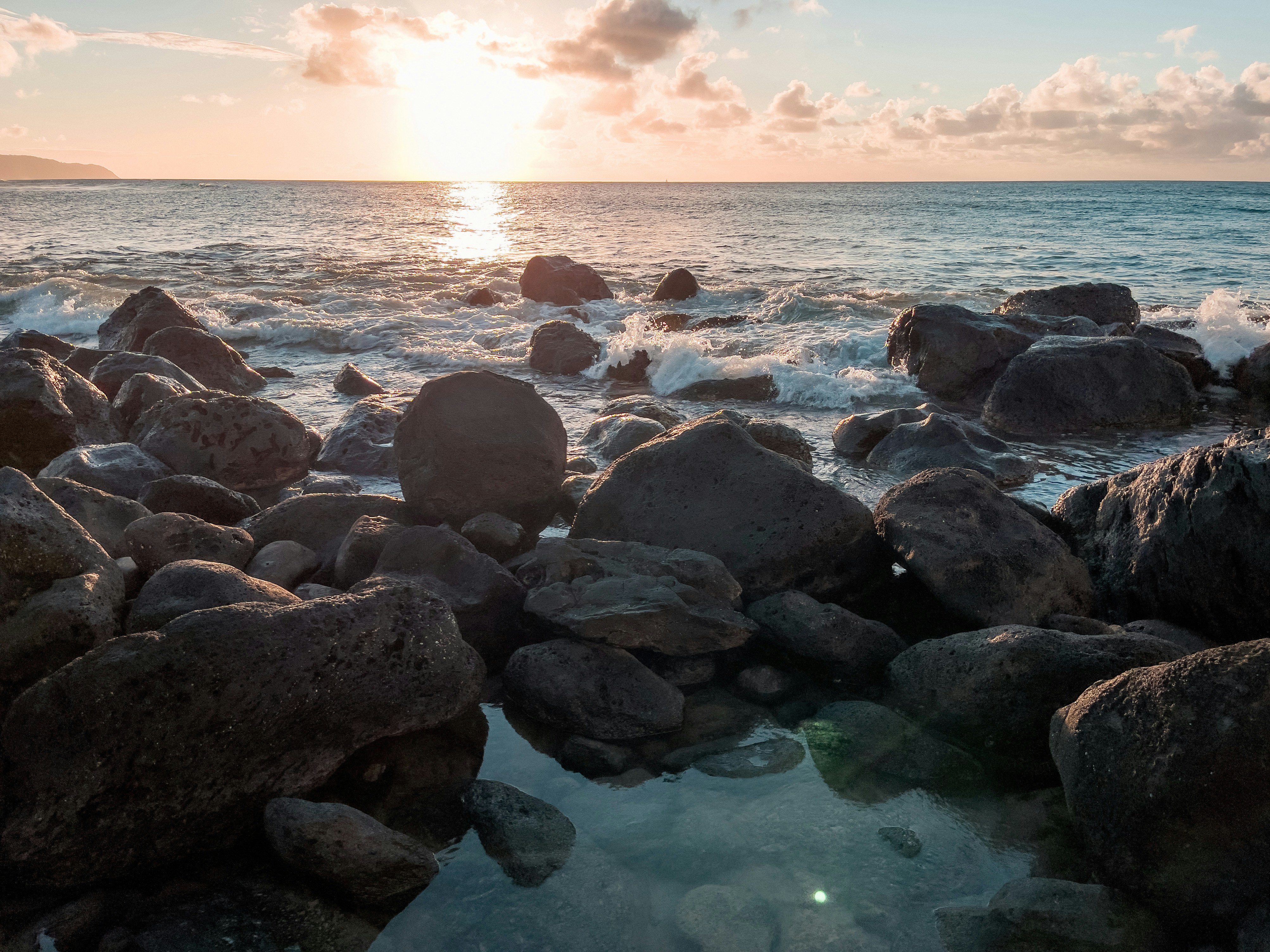Sunset reflecting off the ocean waves, framed by rugged rocks along the shoreline.