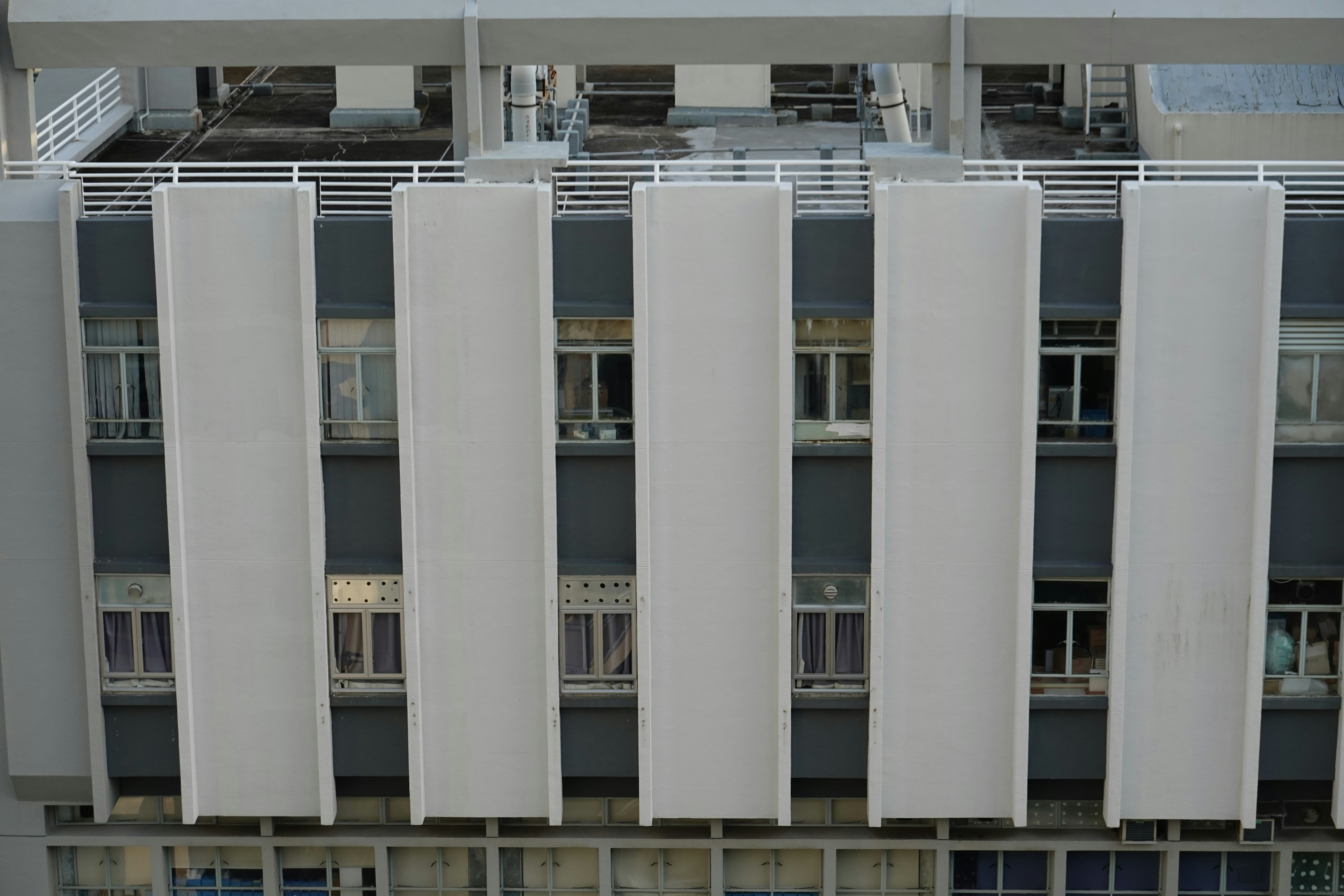 Modern building facade featuring a series of white panels and windows, showcasing urban architecture. The interplay of light and shadows emphasizes the structural design.